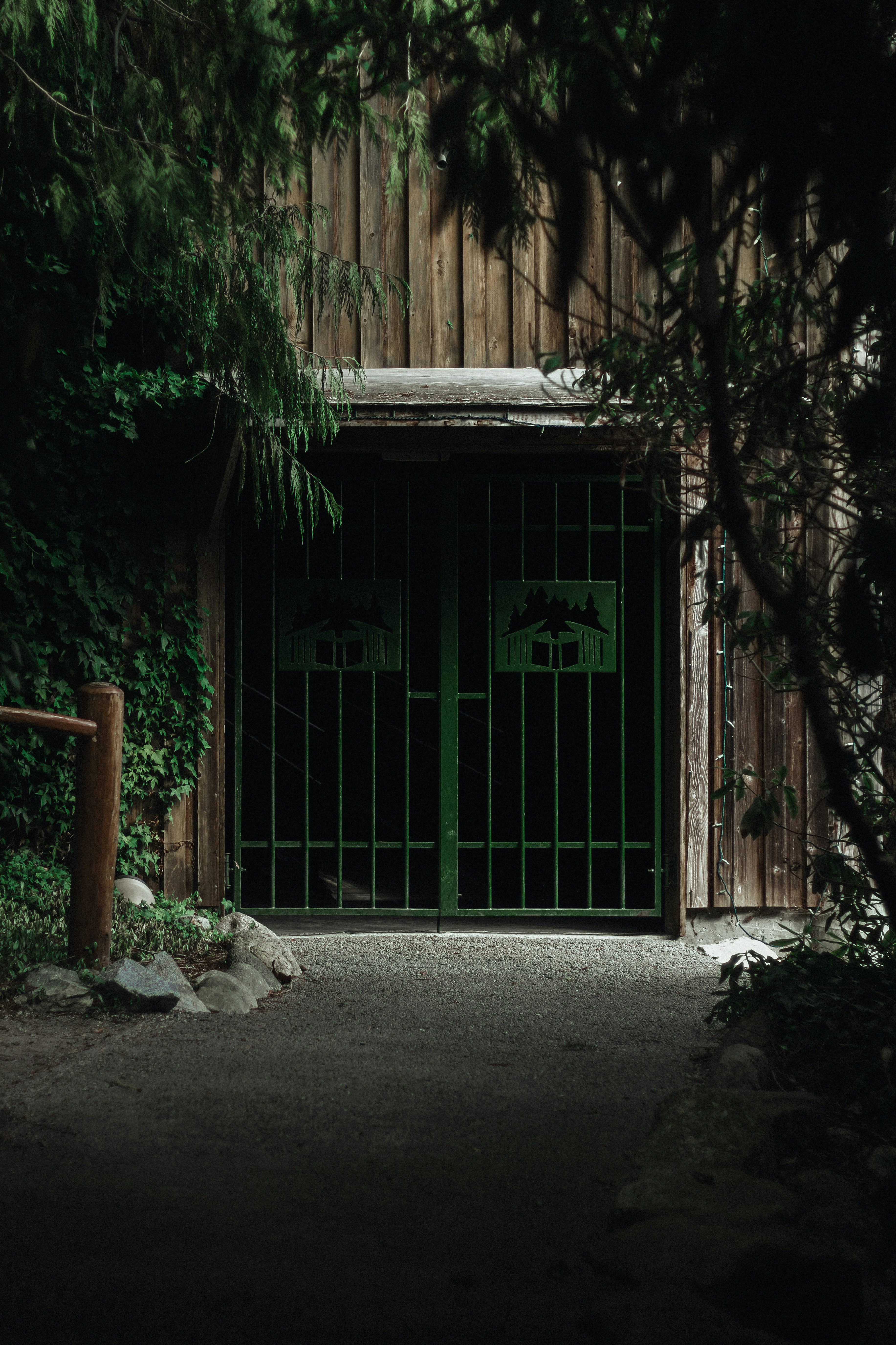 Intricately designed green gates framed by lush foliage, leading into a serene pathway. The natural elements create a peaceful ambiance.
