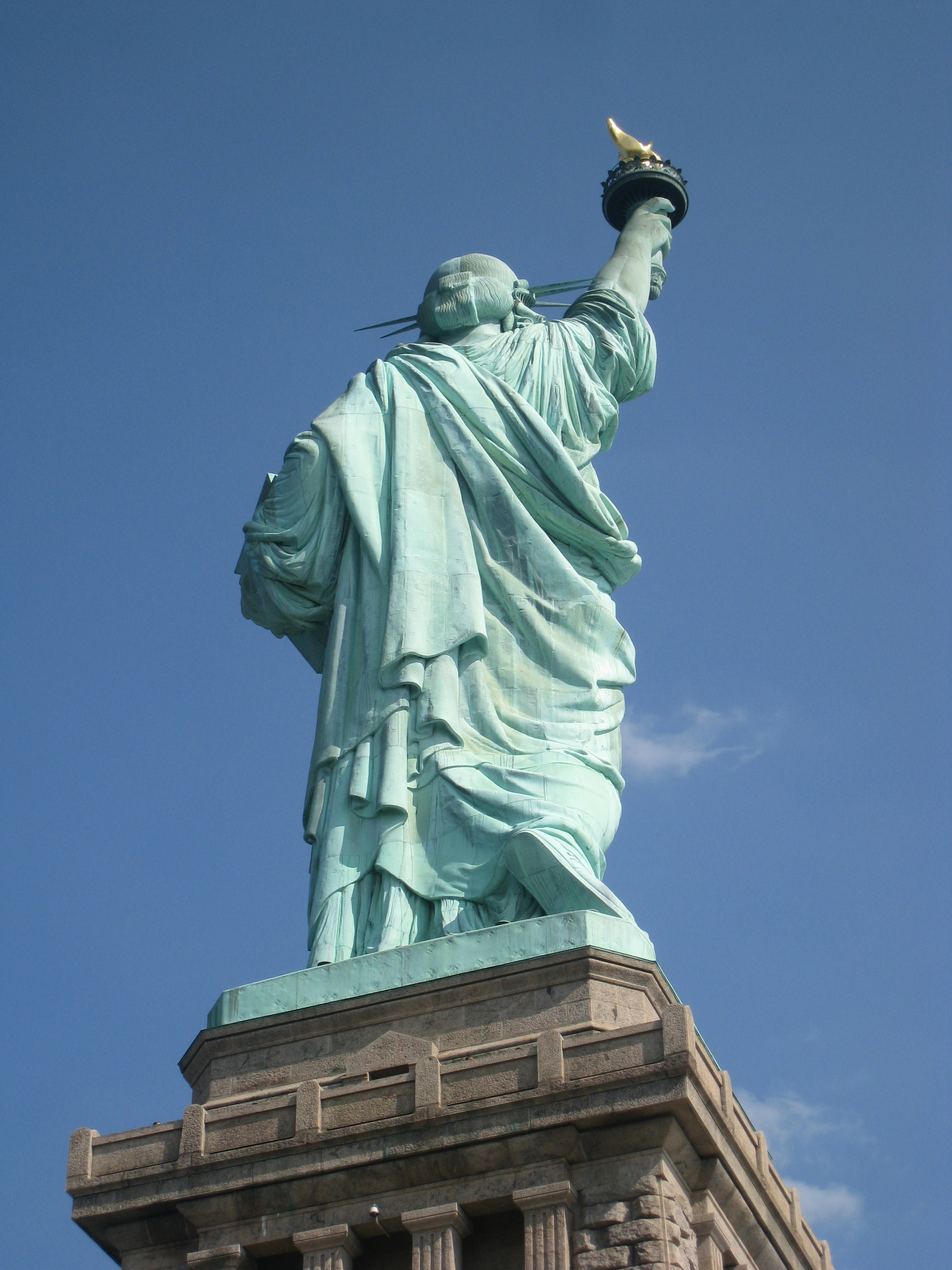 Statue of Liberty standing tall against a clear blue sky, holding her torch aloft. A representation of hope and liberty.