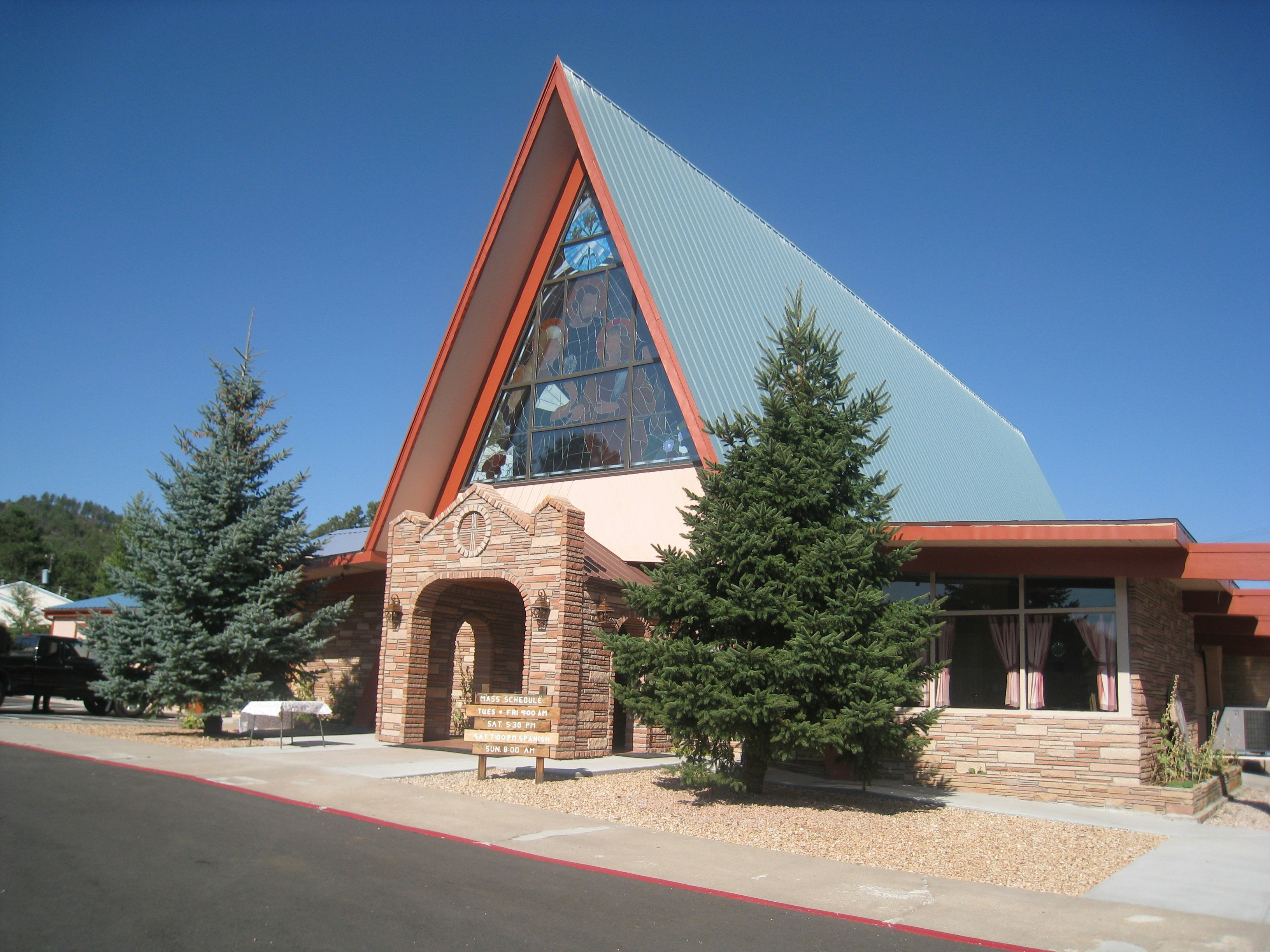 Modern A-frame building with a striking glass facade and surrounding evergreen trees, showcasing a blend of natural and architectural beauty.
