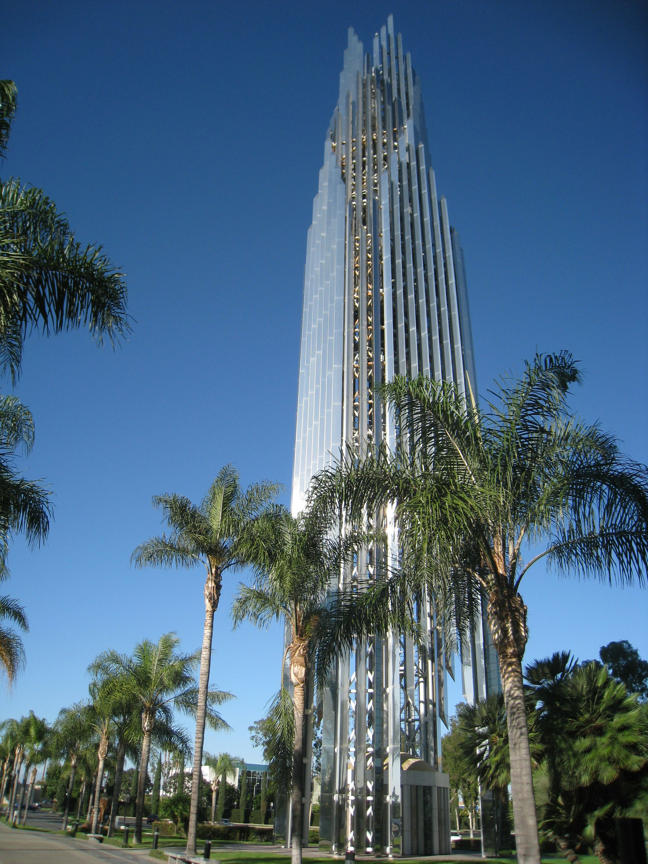 A sleek, modern skyscraper towers over a row of palm trees under a clear blue sky. The structure's reflective surface captures the surrounding greenery.