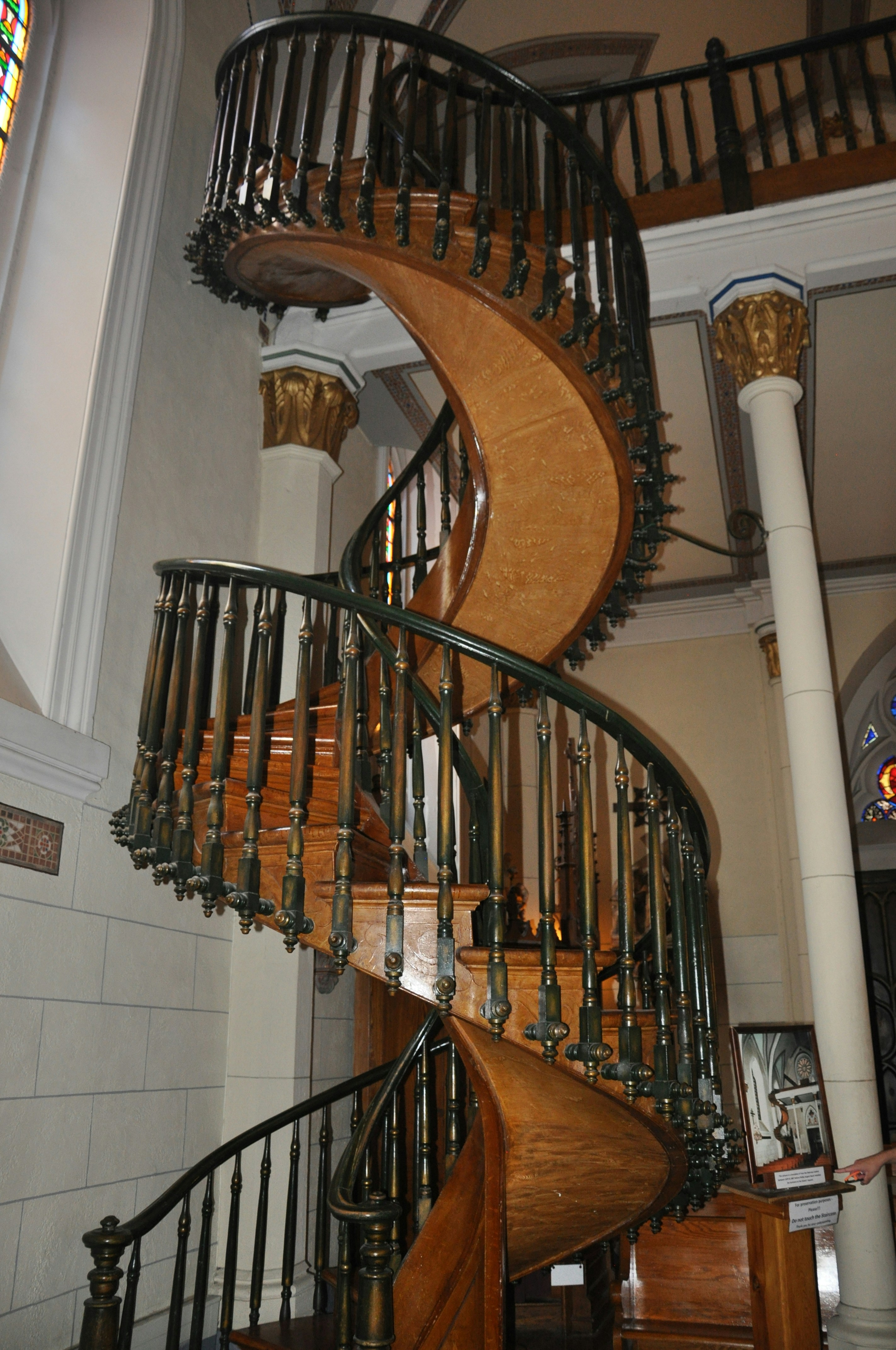 Intricate wooden spiral staircase with ornate railings, showcasing craftsmanship within a historical building.
