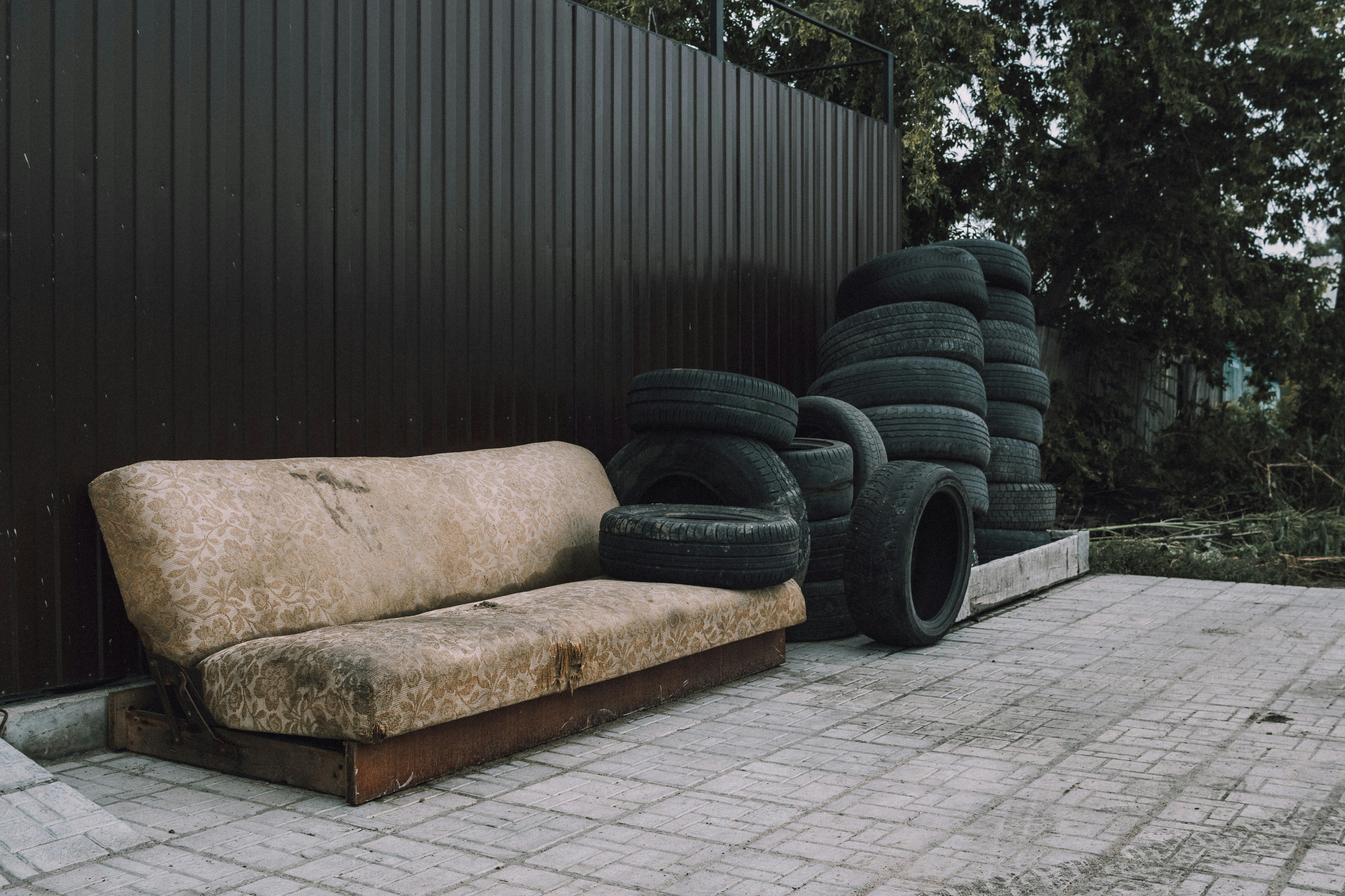 Worn-out couch resting against a backdrop of stacked tires in an urban setting, highlighting the contrast between comfort and decay.