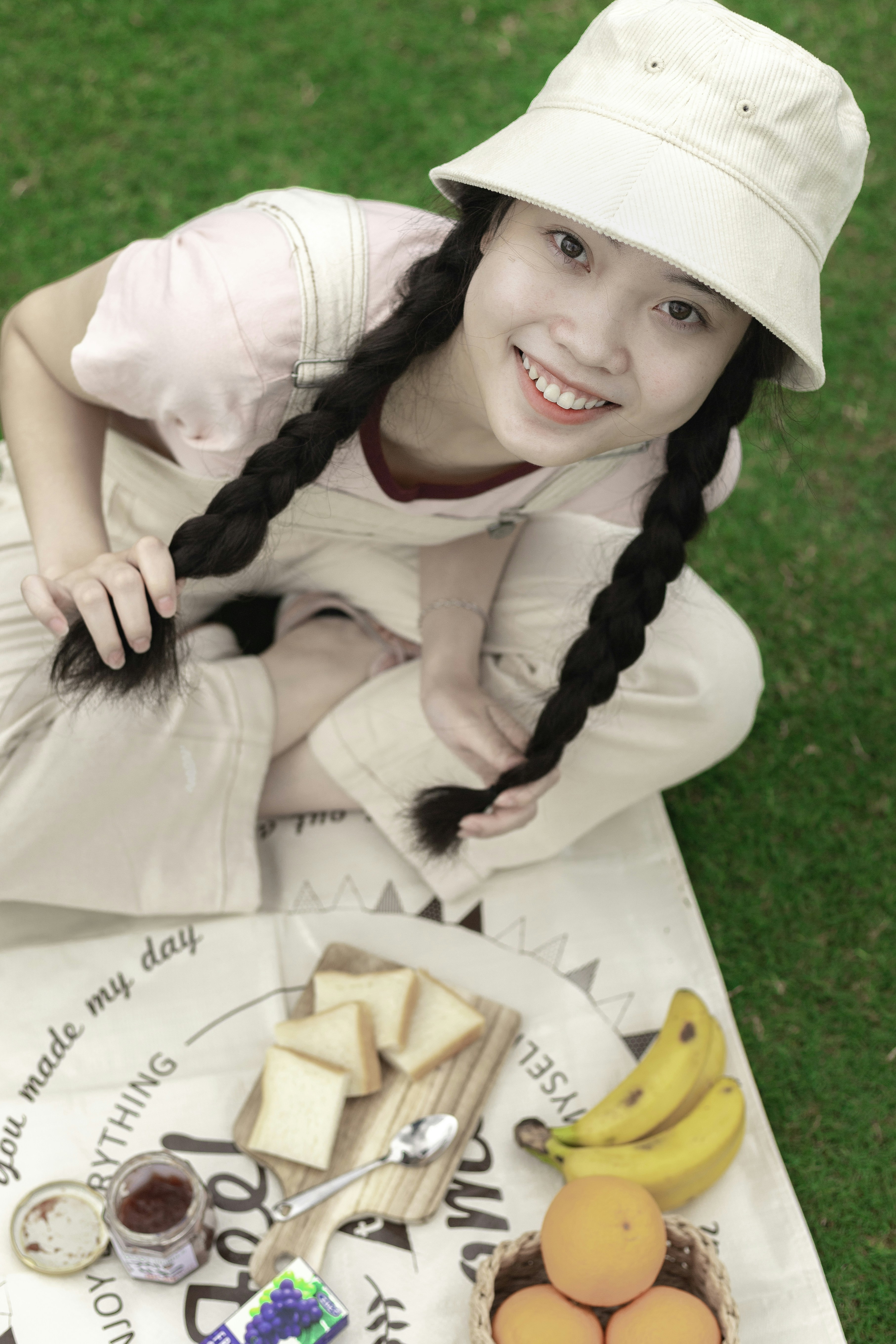 Young woman with braided hair enjoying a picnic on a blanket, surrounded by fruits and snacks.