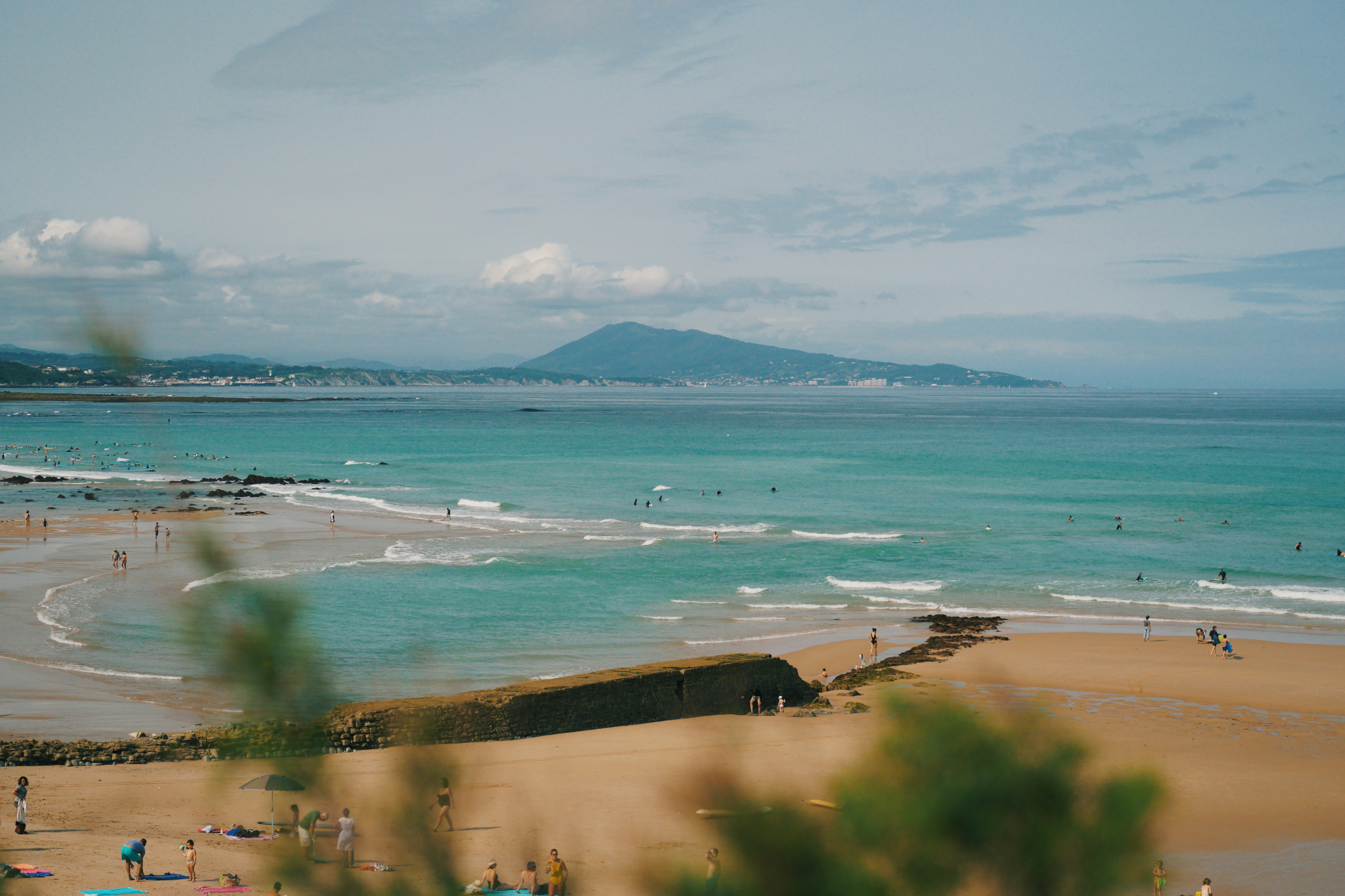 Vibrant beach scene with surfers riding waves and people enjoying the sandy shore under a clear sky.