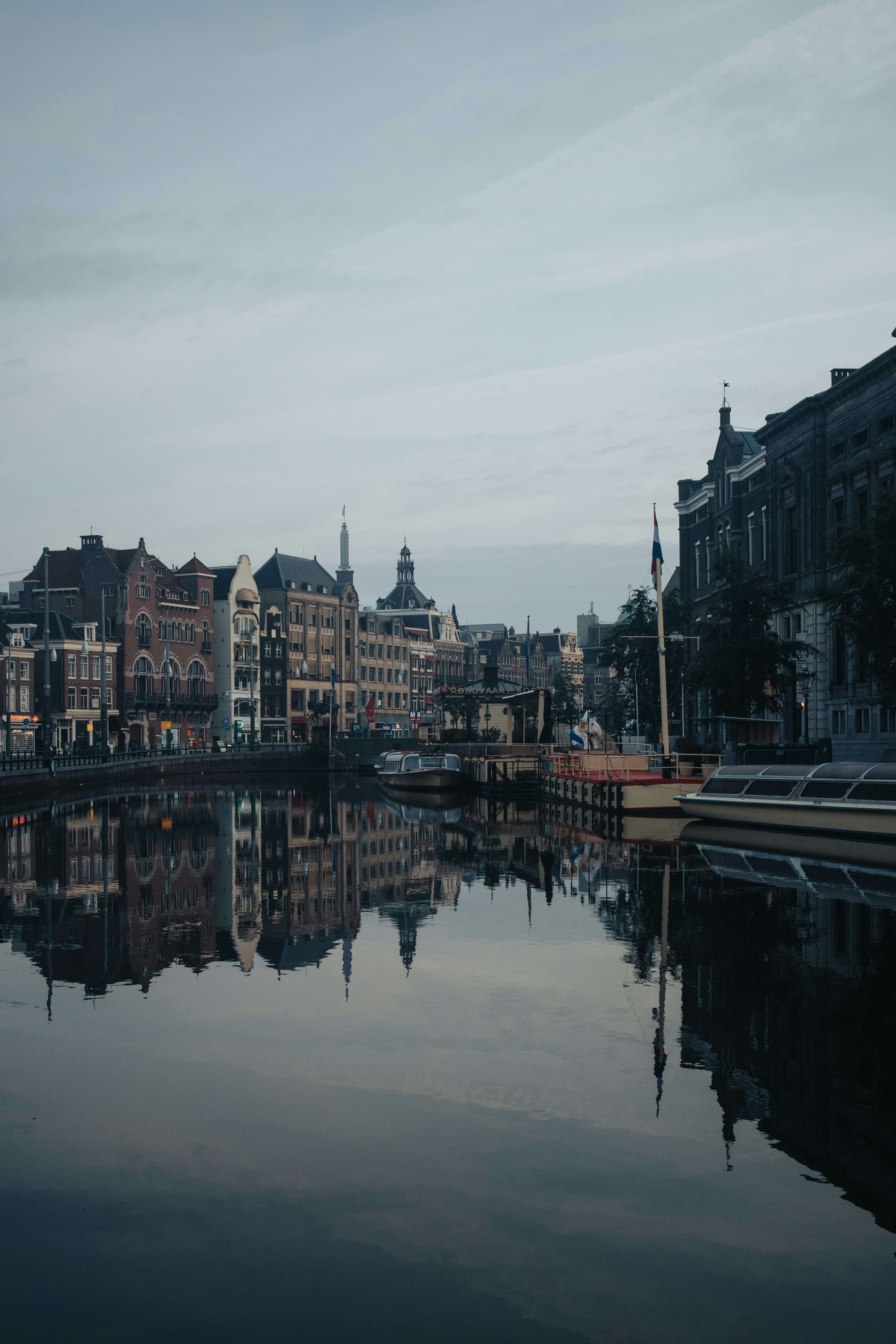 Historic buildings lining a tranquil canal, creating a mirror-like reflection under a soft morning sky.