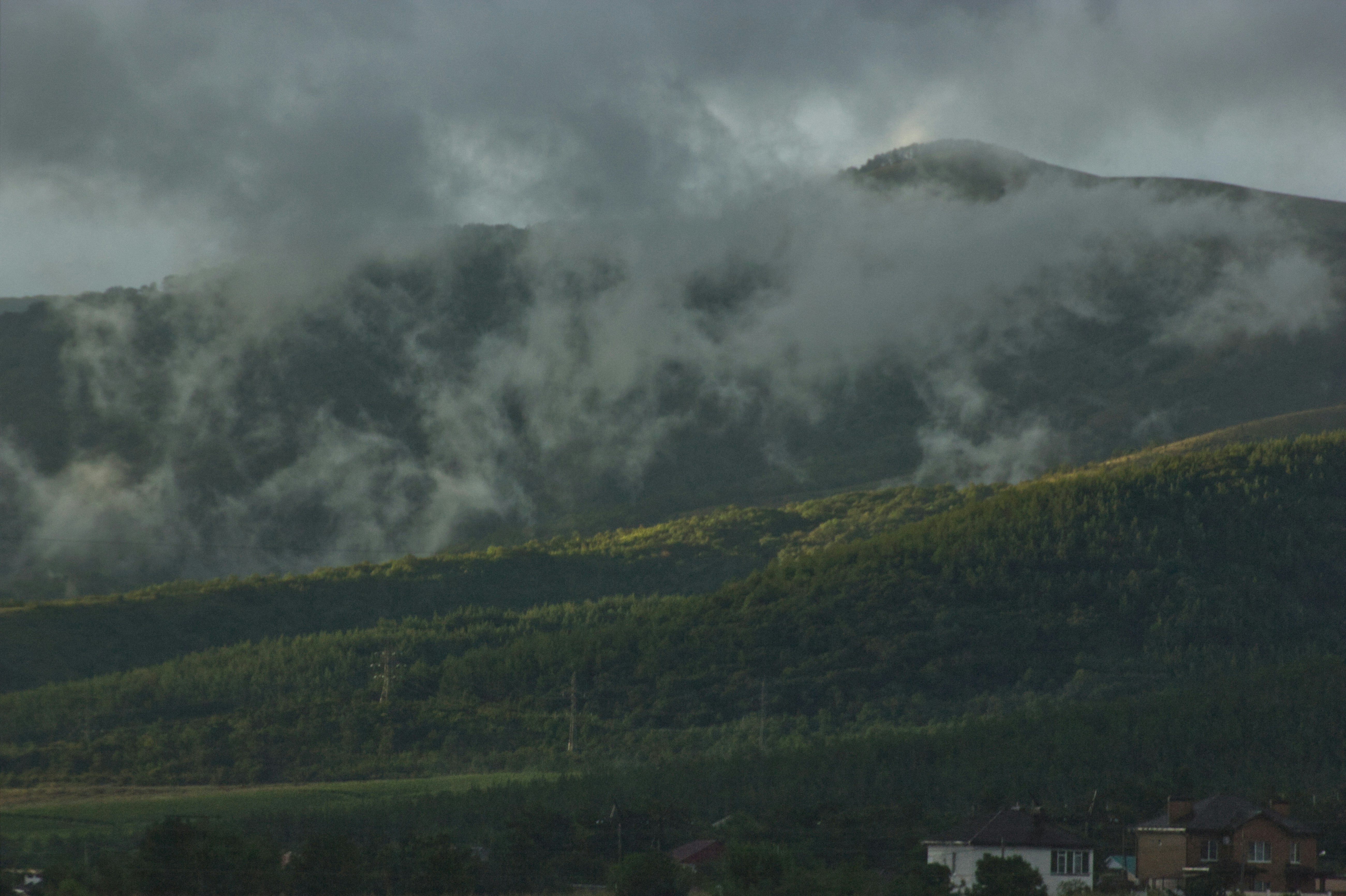 Misty mountains shrouded in clouds with a lush green landscape below, capturing the serene beauty of nature's transitions.