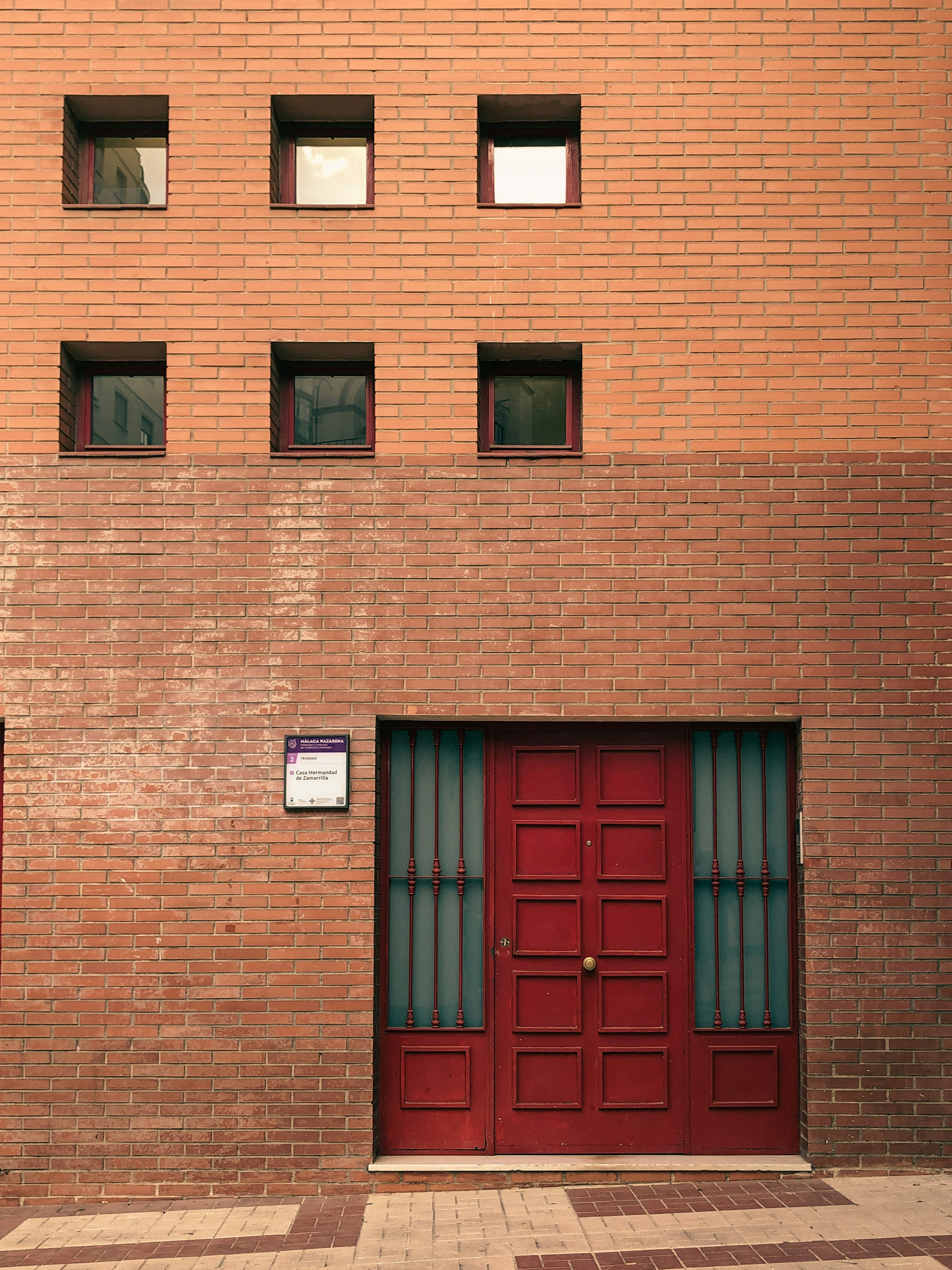 Brick wall featuring a prominent red door flanked by smaller windows, creating a striking architectural contrast. A street sign adds context to the urban setting.