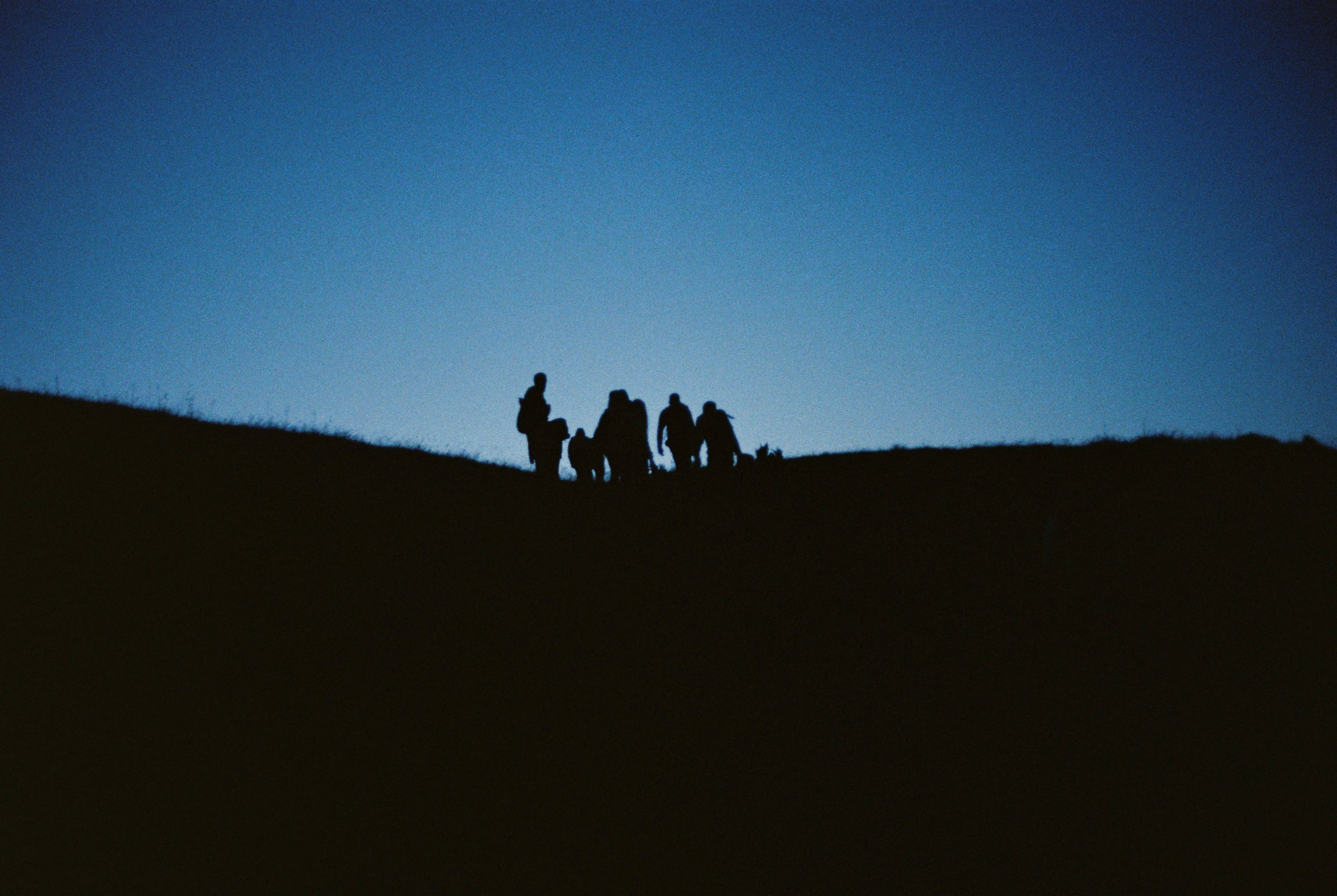 Silhouetted figures walking along a ridge against a deep blue twilight sky.