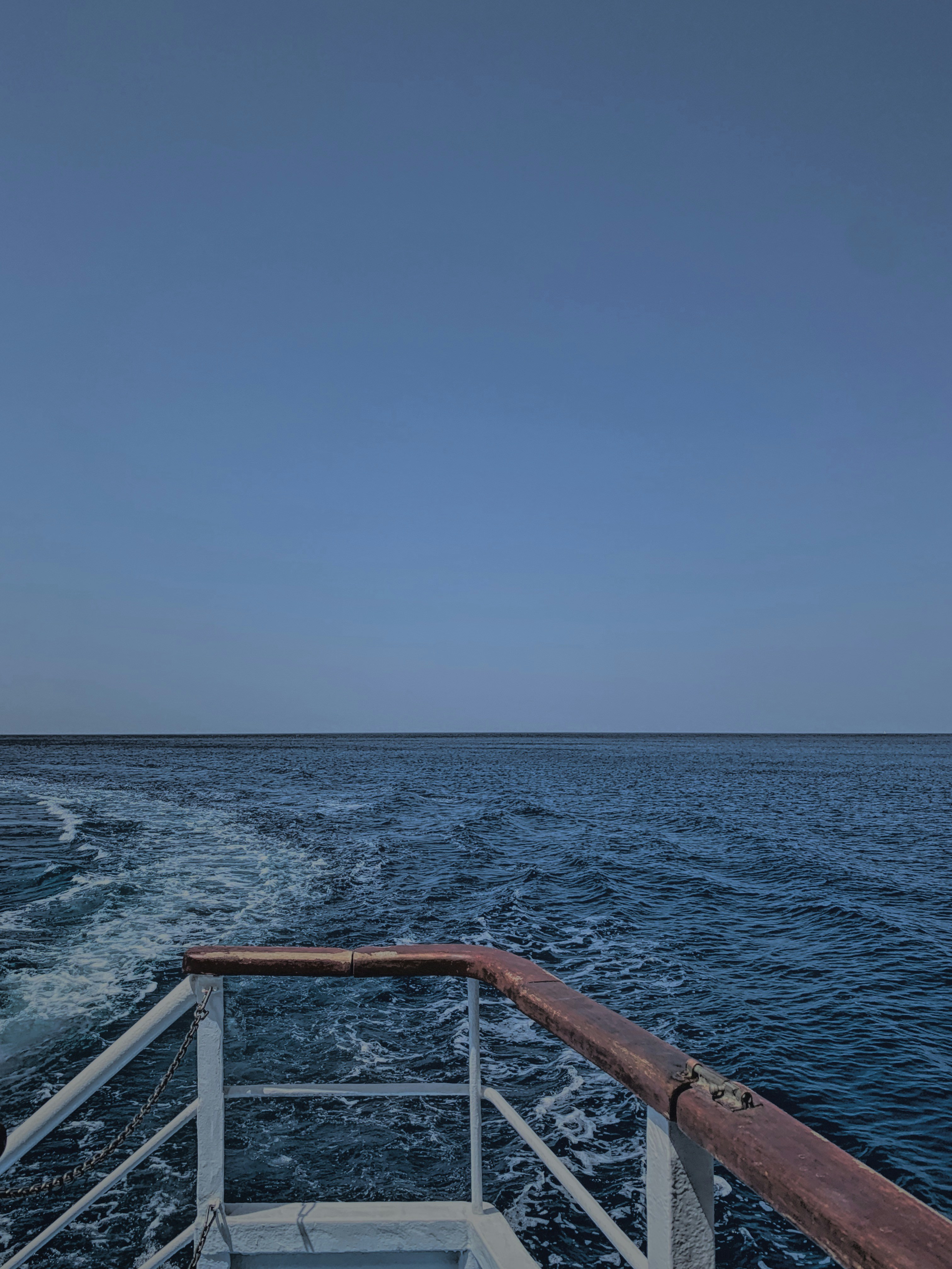 Boat's railing with wake trailing behind, set against a vast blue sea and clear sky.