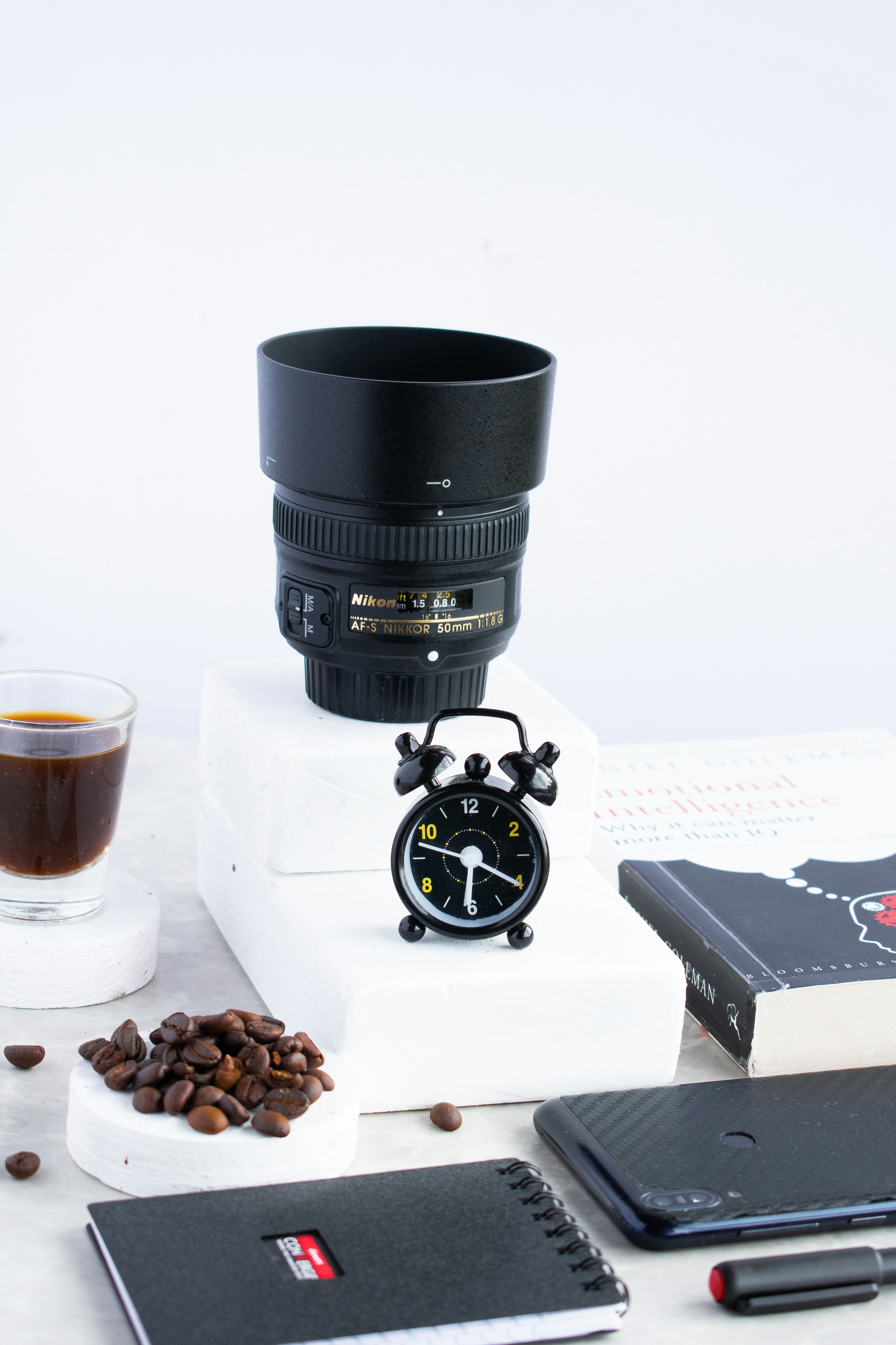 Focused Still Life: A Nikon Lens, Coffee, and Clock on White Pedestal