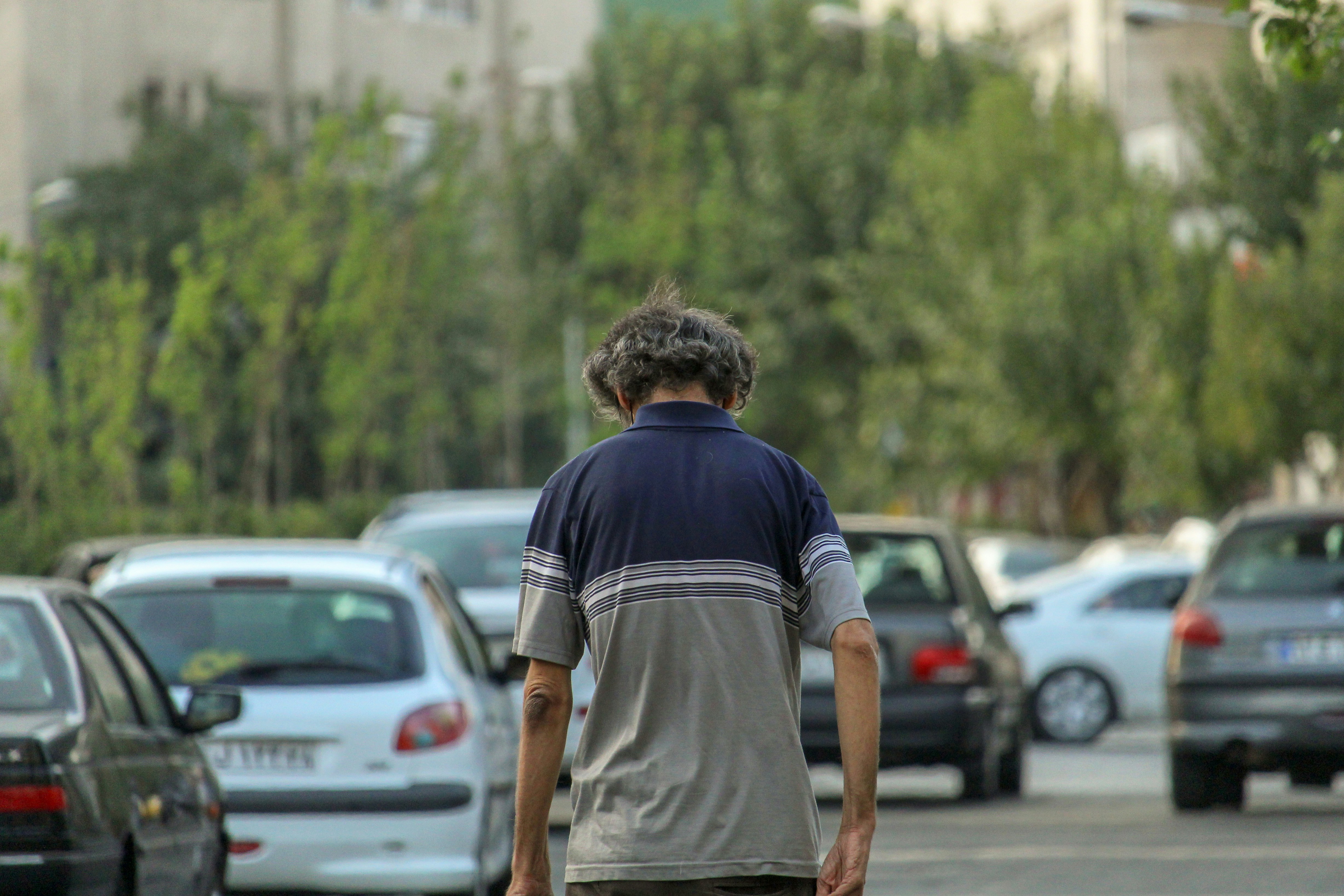 Person walking through a parking lot with trees in the background.