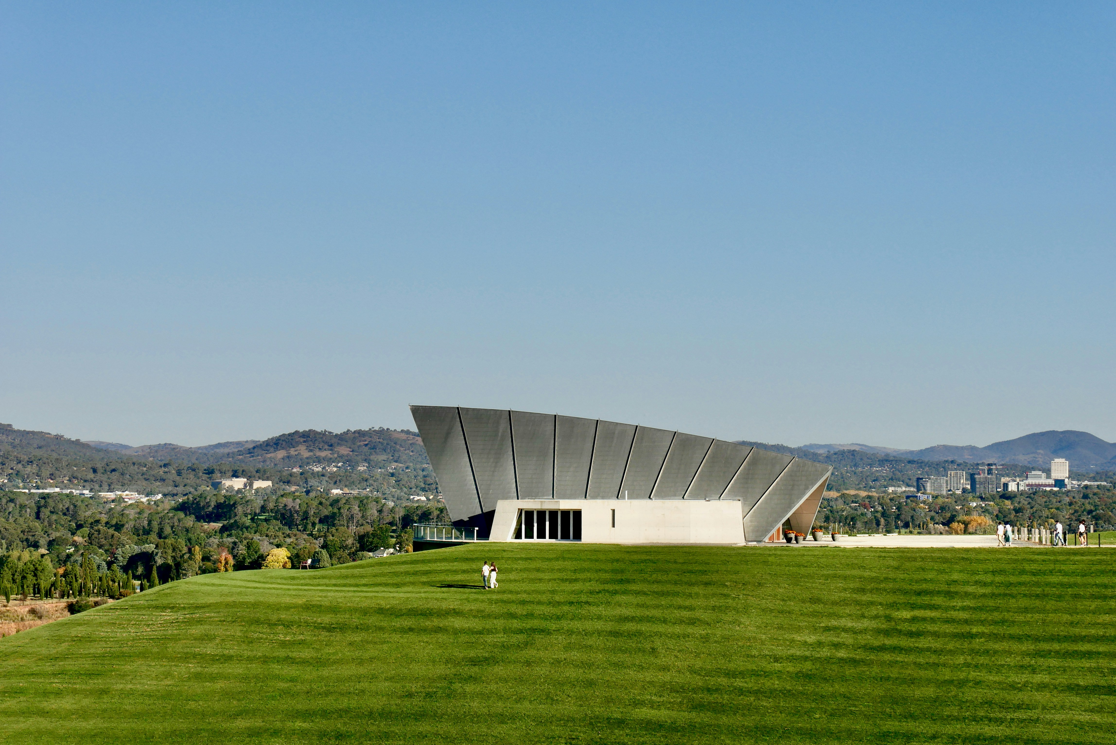 Modern building with a striking angular design set against a backdrop of rolling hills and clear blue sky.
