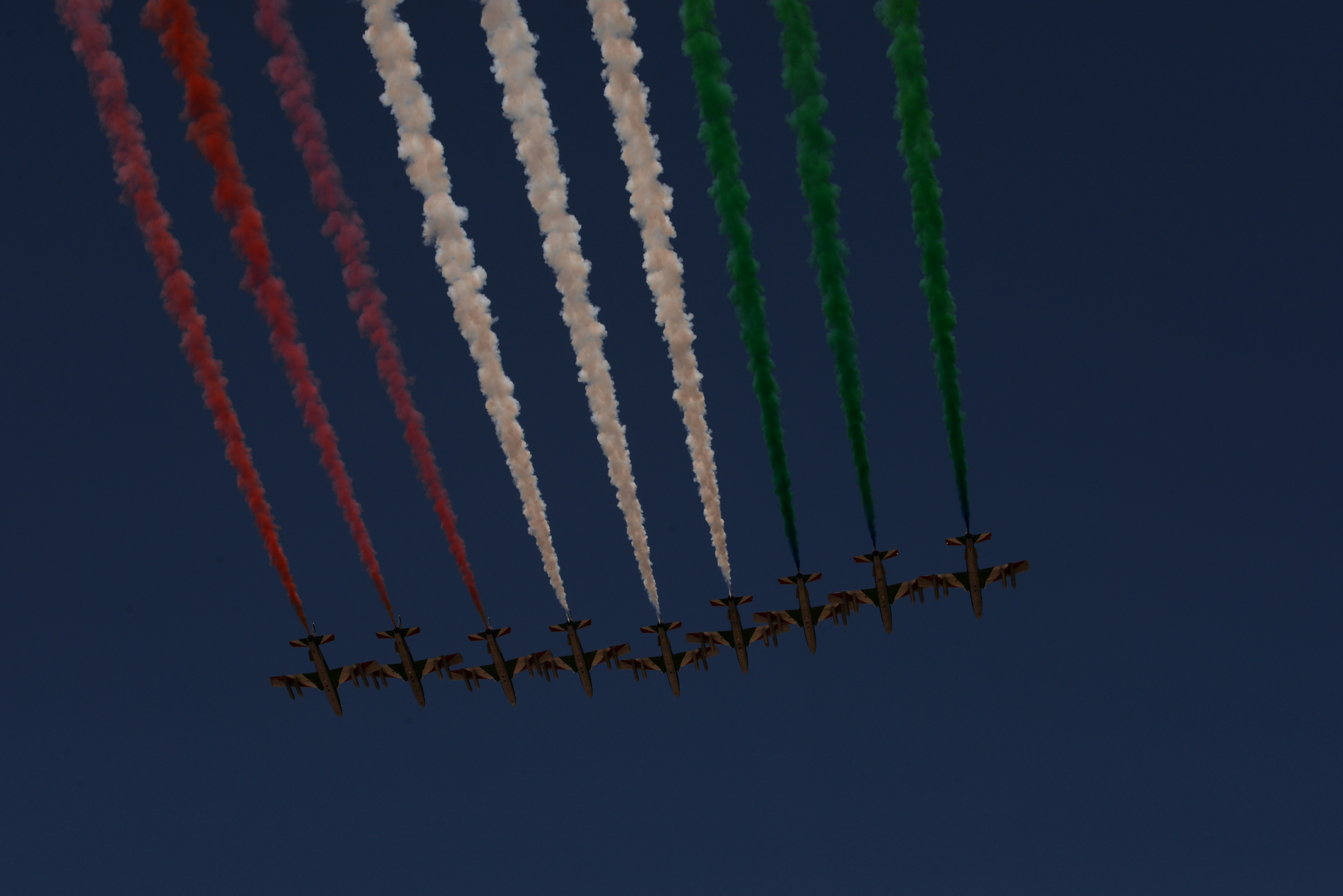 Aircraft in formation trail vibrant red, white, and green smoke against a clear blue sky.