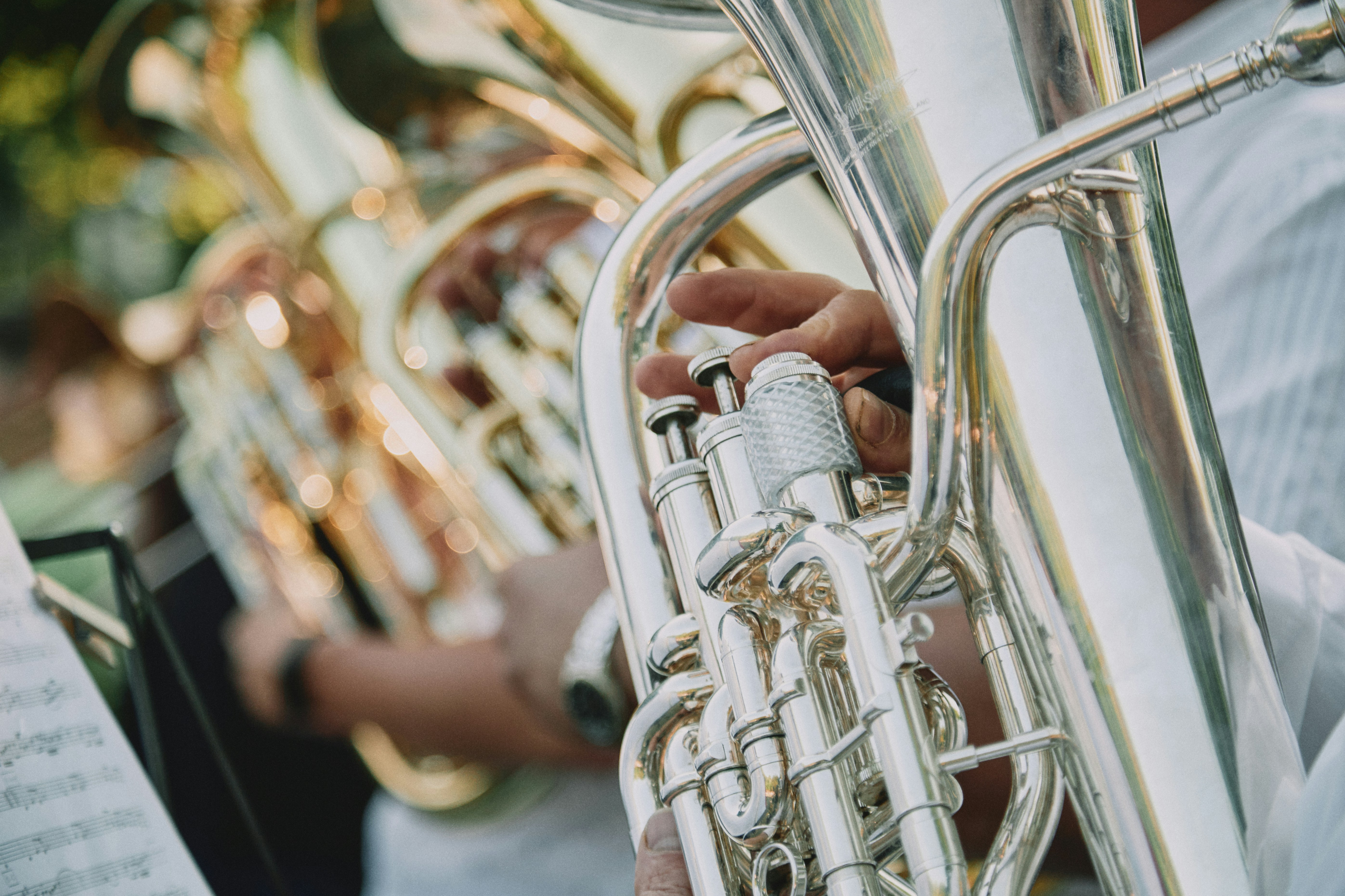 Musicians playing shiny brass instruments outdoors, with sunlight reflecting off the metal.