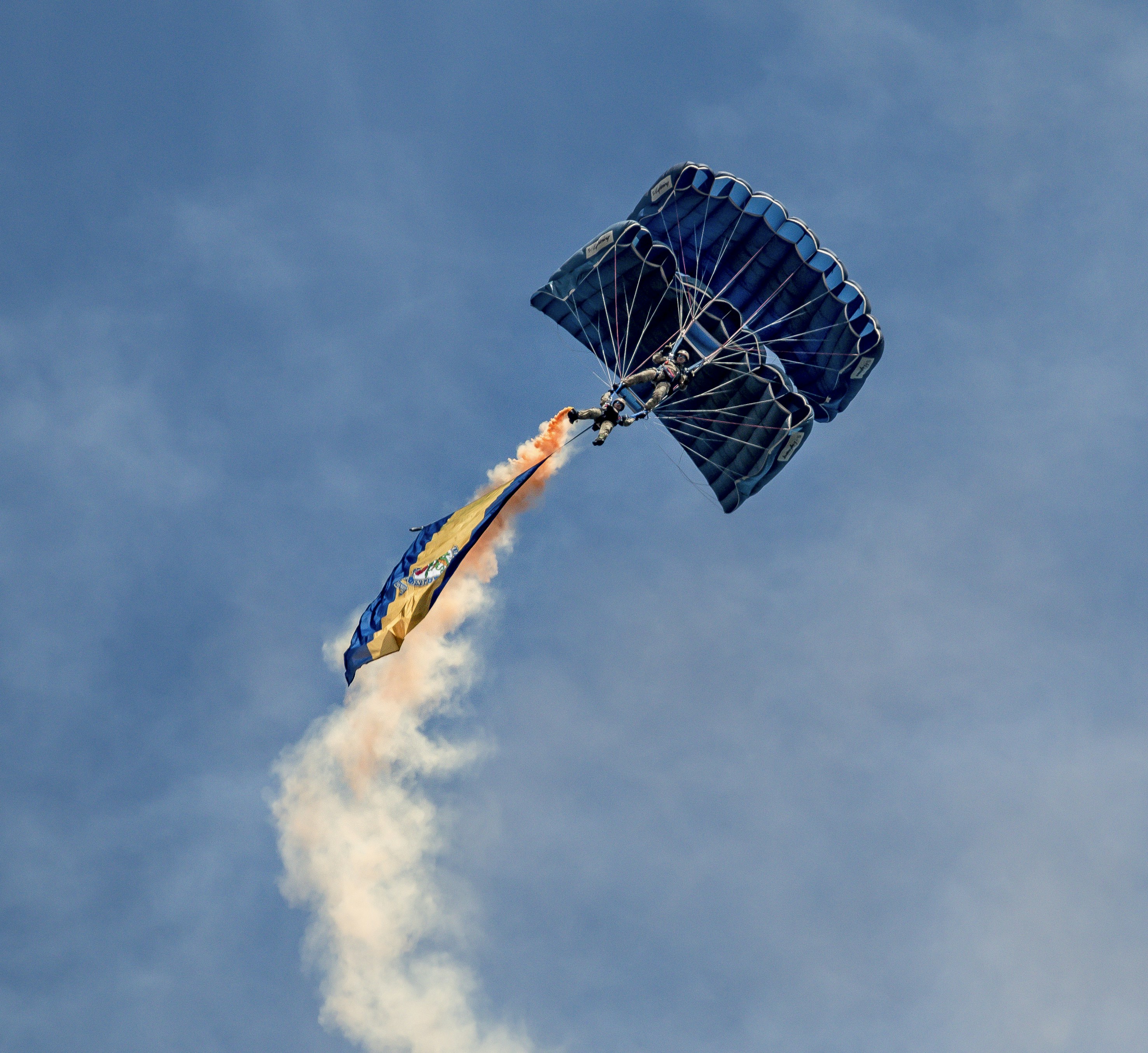 Blue Parachute Descent: Orange Smoke Traces a Skyward Arc
