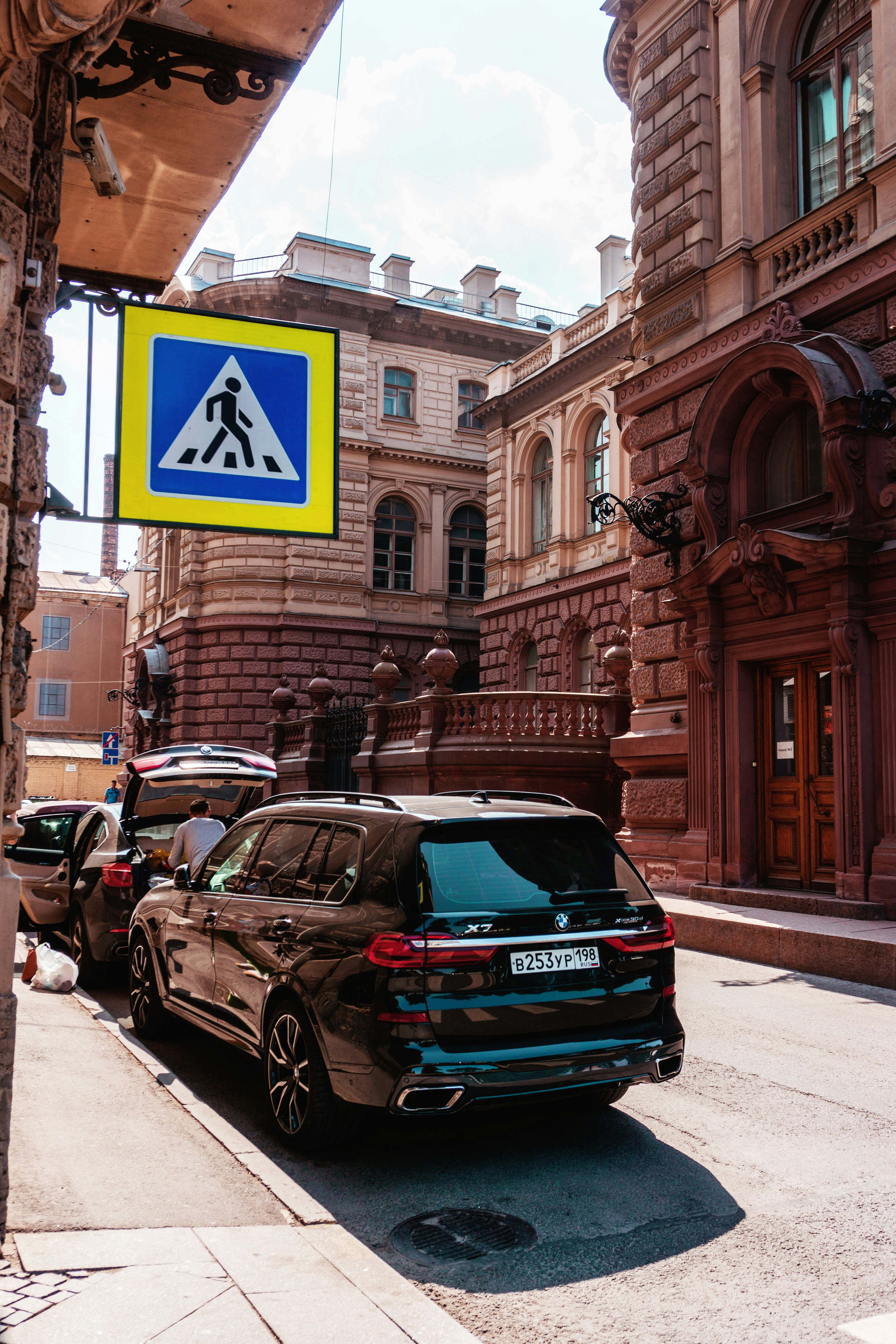 A sleek black SUV parked alongside historic architecture, with a pedestrian crossing sign overhead. The scene captures the blend of modernity and tradition in a bustling city.
