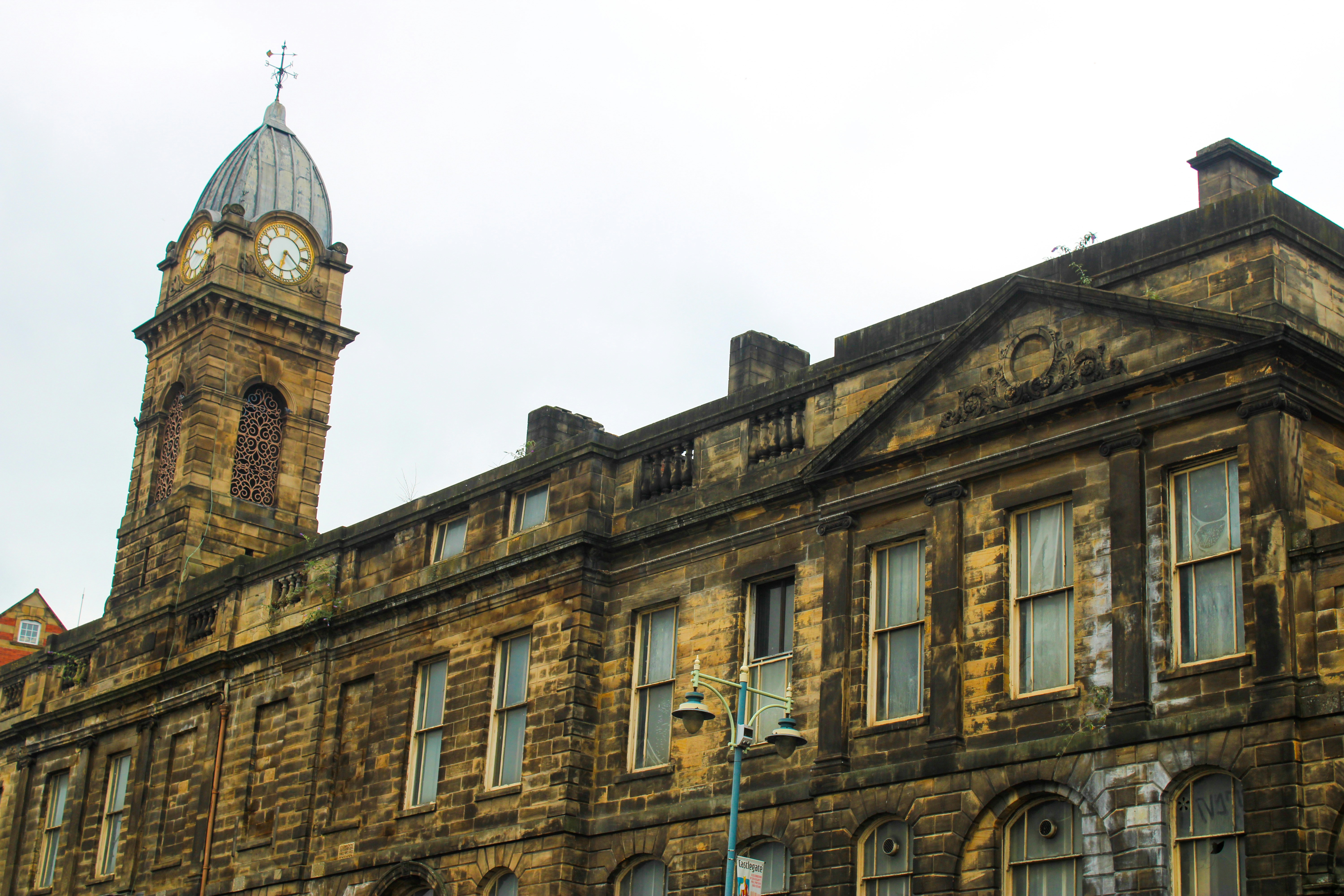 Historic brown stone building with a prominent clock tower under a cloudy sky.