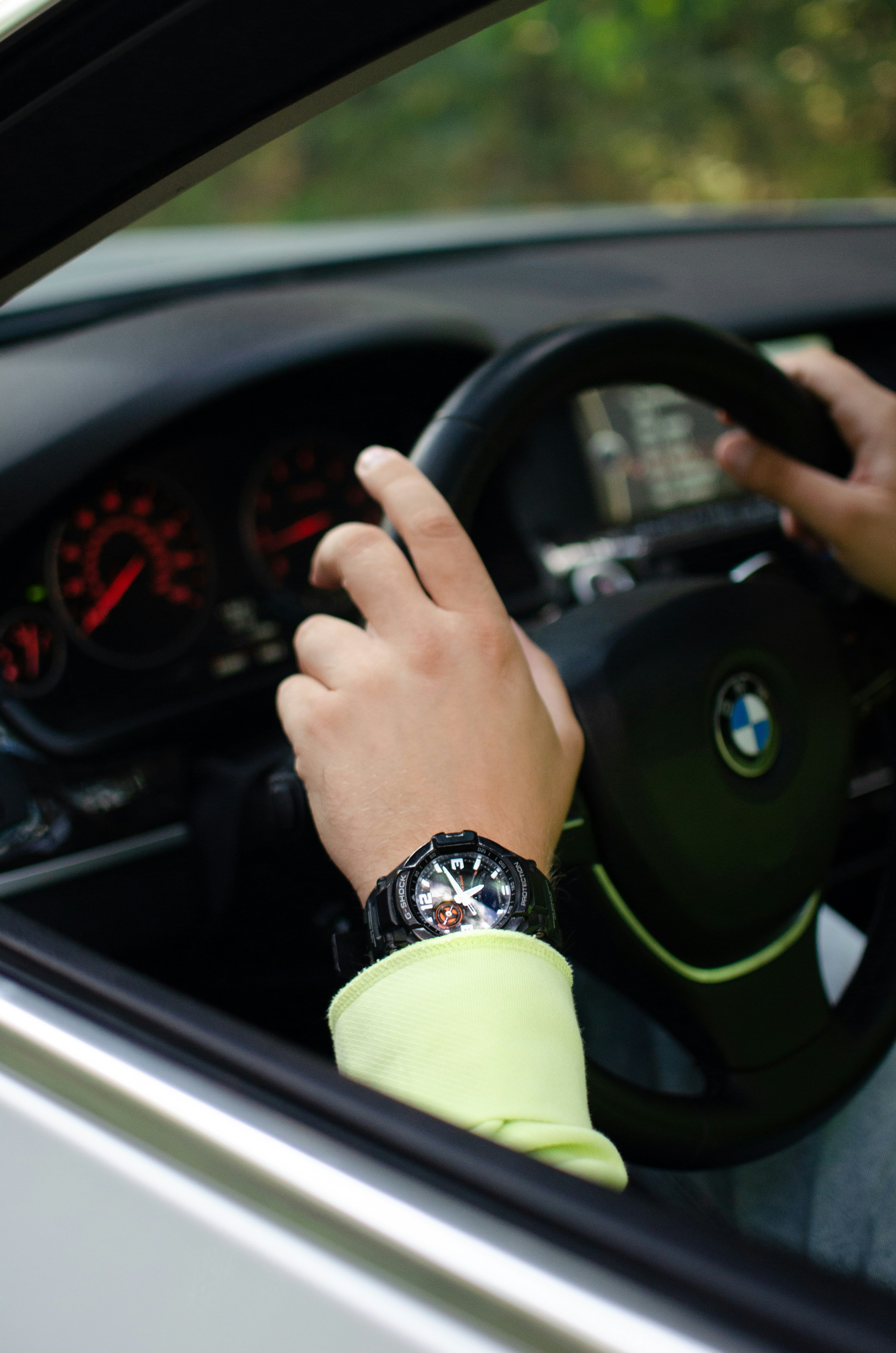 Close-up of a driver's hand on the steering wheel, showcasing a stylish wristwatch and the dashboard of a BMW vehicle.