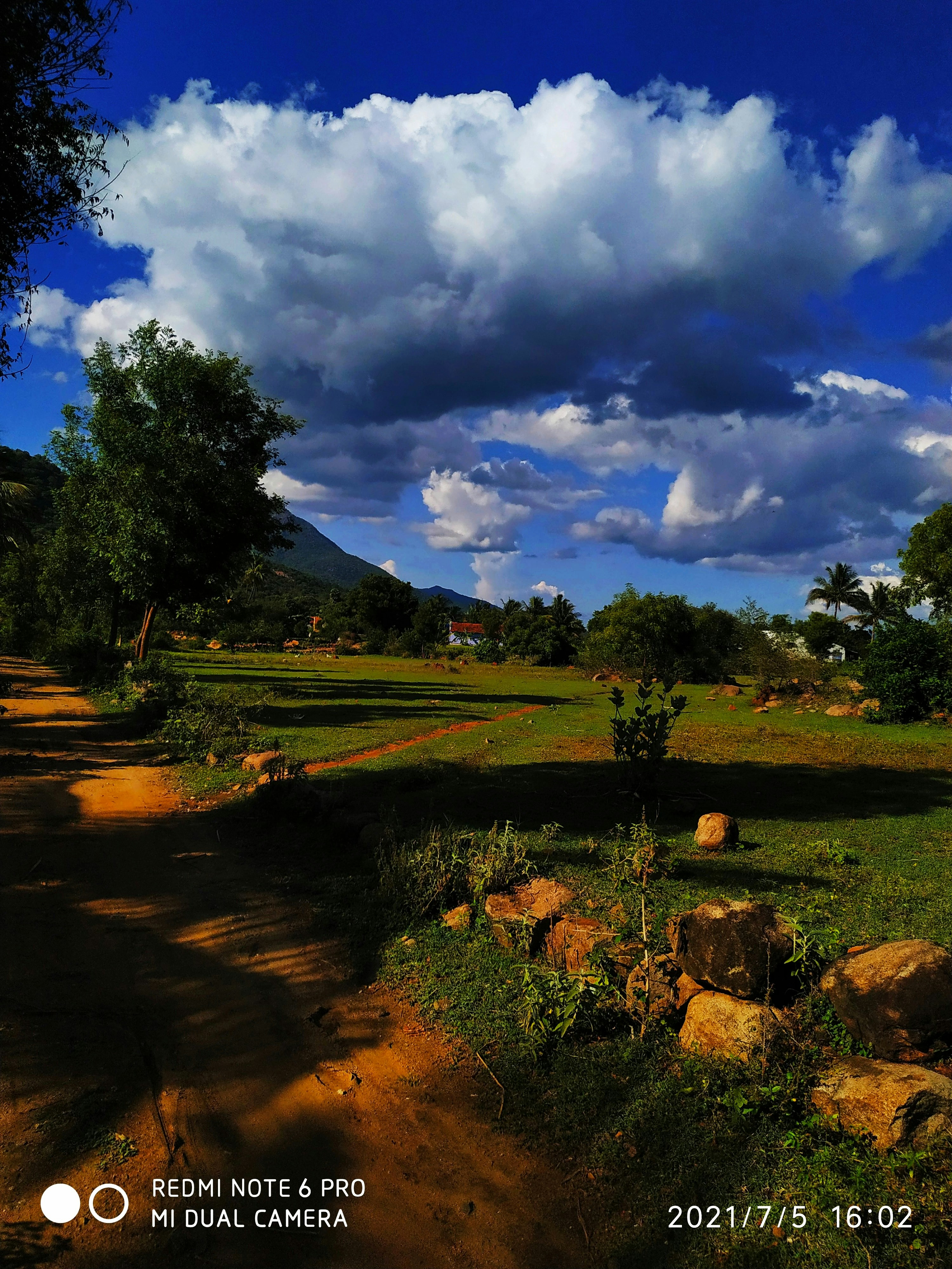 Dusty Path through a Sunlit Pastoral Valley Beneath a Sky of Dramatic Clouds