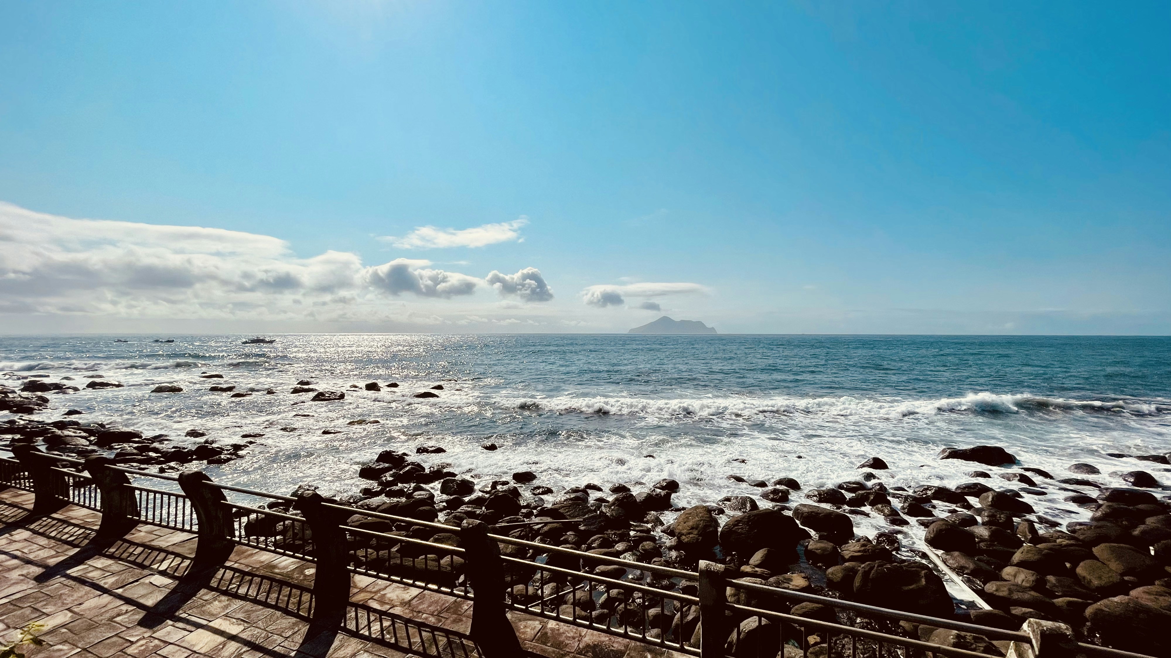 Seaside Promenade: Silhouette Against a Blue Horizon and Foam-Flecked Rocks