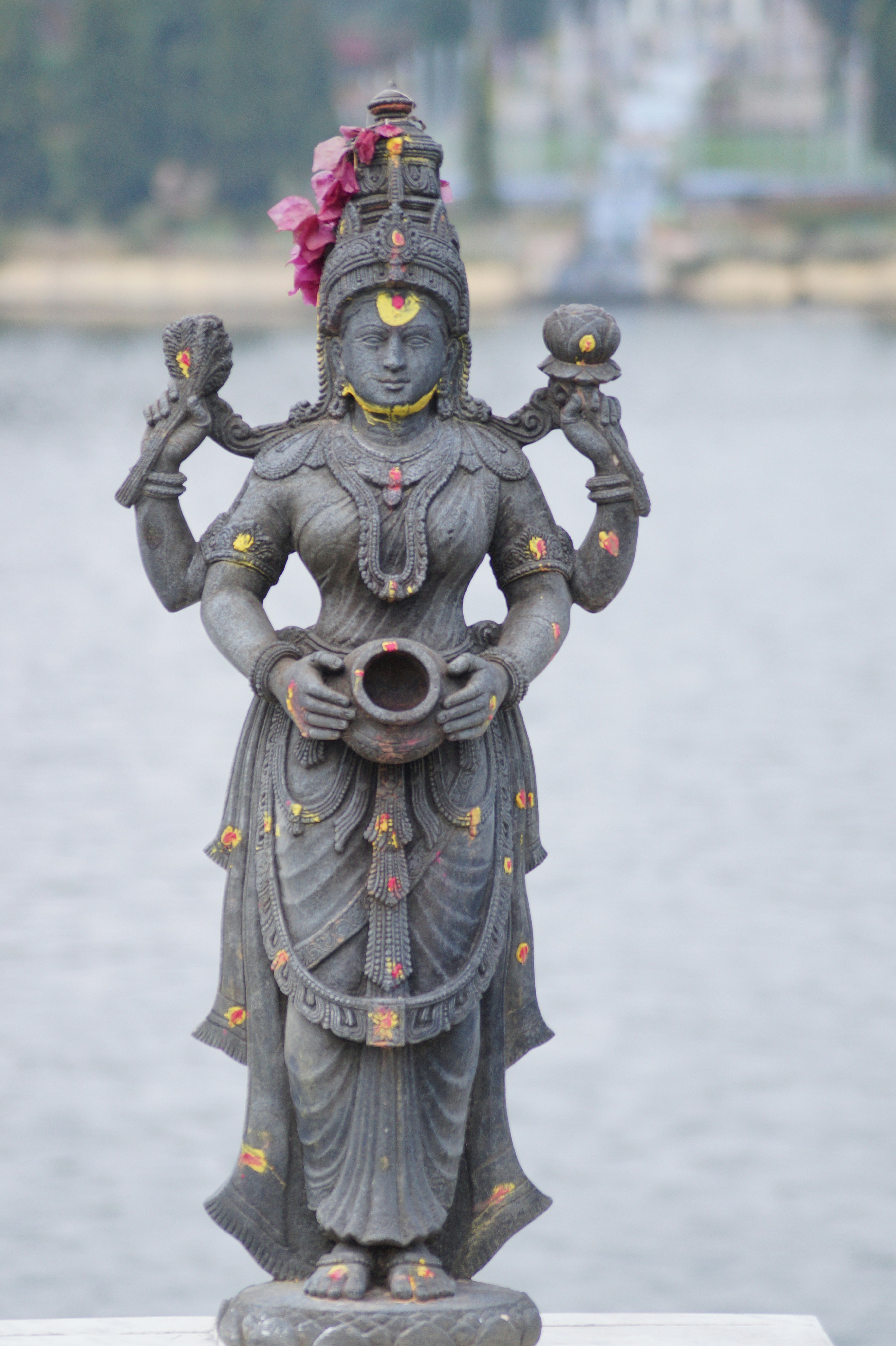 Lakeside Reverence: Four-Armed Stone Goddess Adorned with Petals