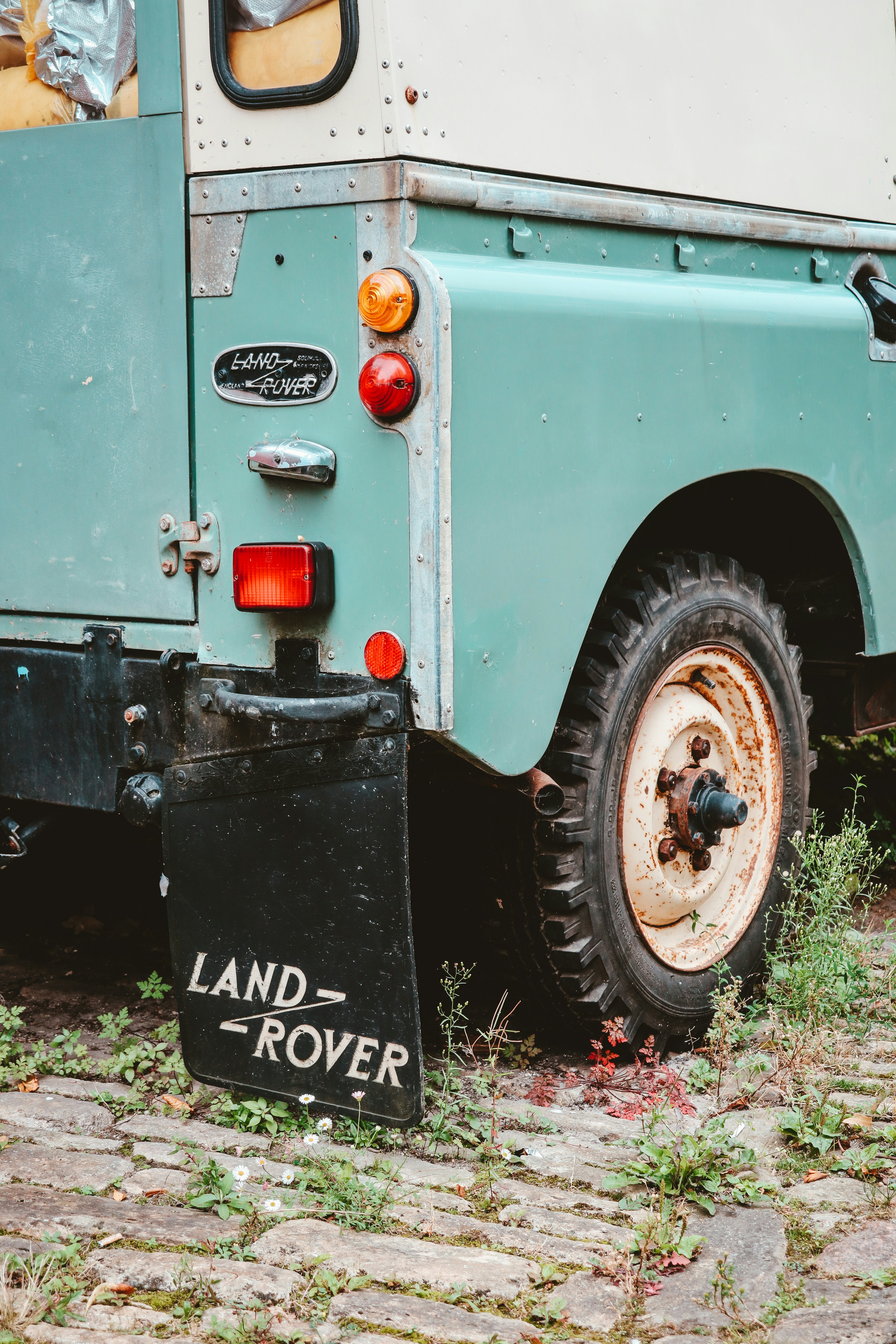 Vintage Land Rover parked amidst overgrown cobblestones, showcasing its classic design and rugged charm.