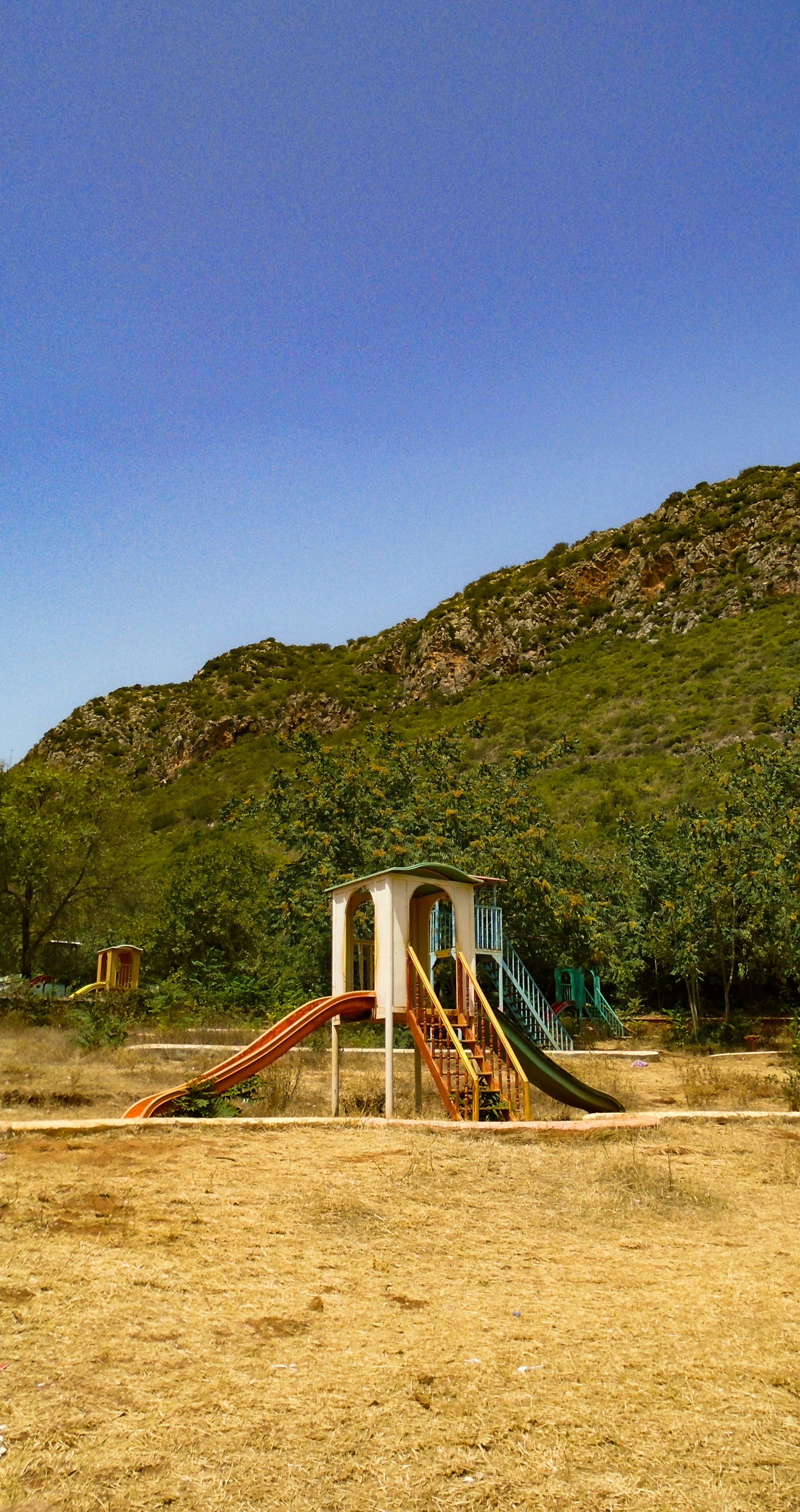 Colorful playground structure with slides set against a backdrop of rolling hills and clear blue sky.