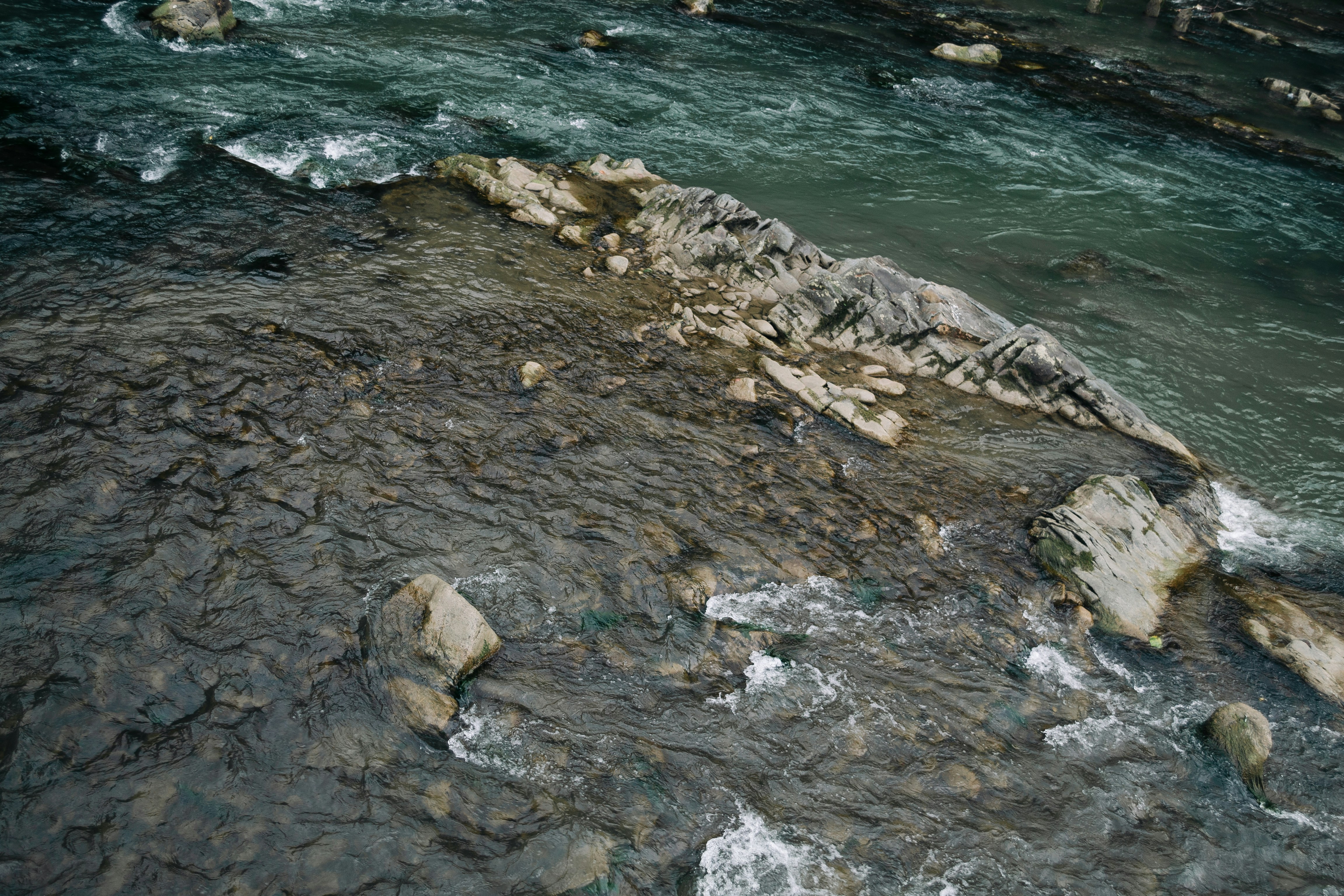 A serene river flows over textured rocks, showcasing the contrast between water and stone in a tranquil natural setting.