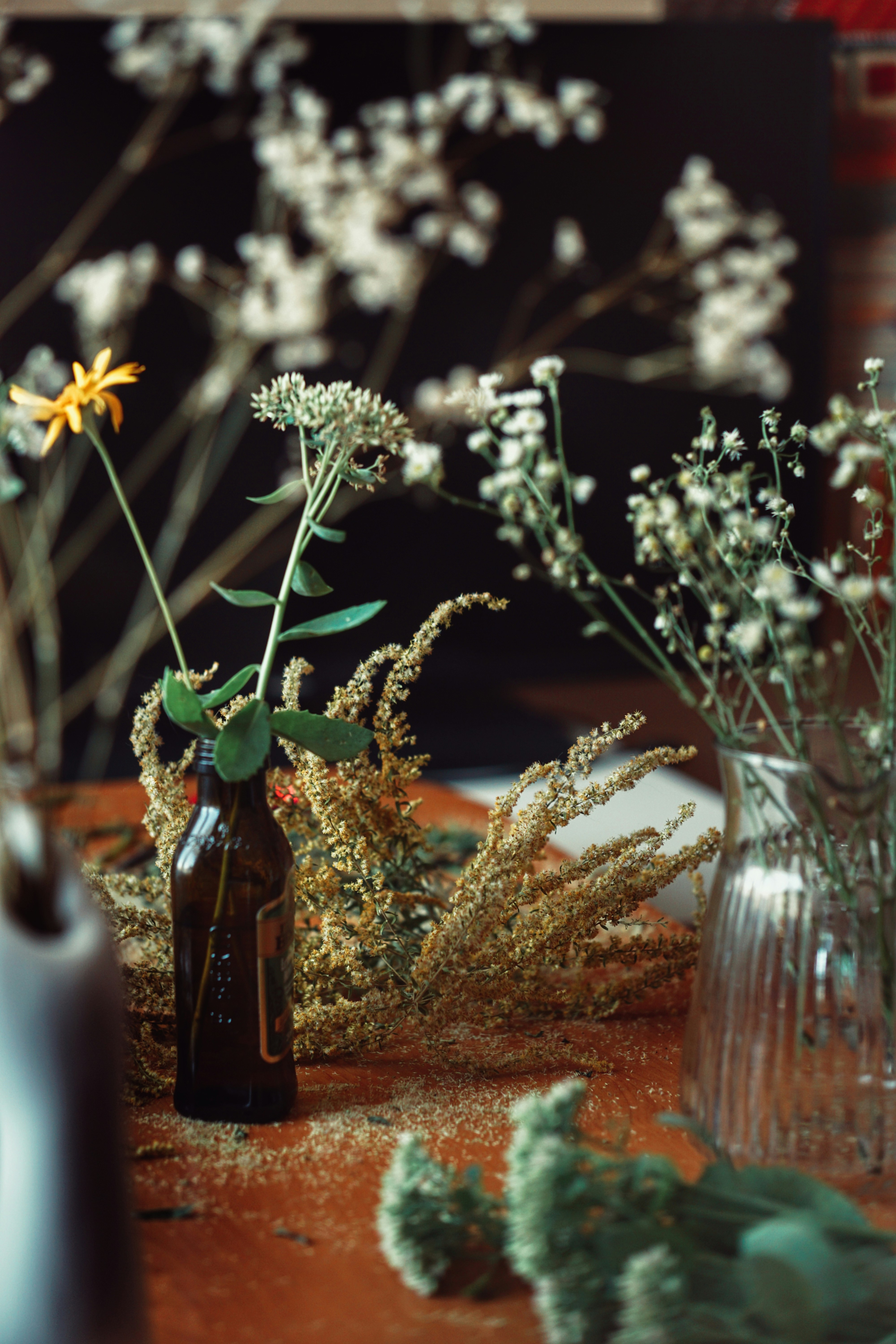 A delicate arrangement of wildflowers and foliage in various vases on a rustic wooden table, creating an inviting atmosphere.