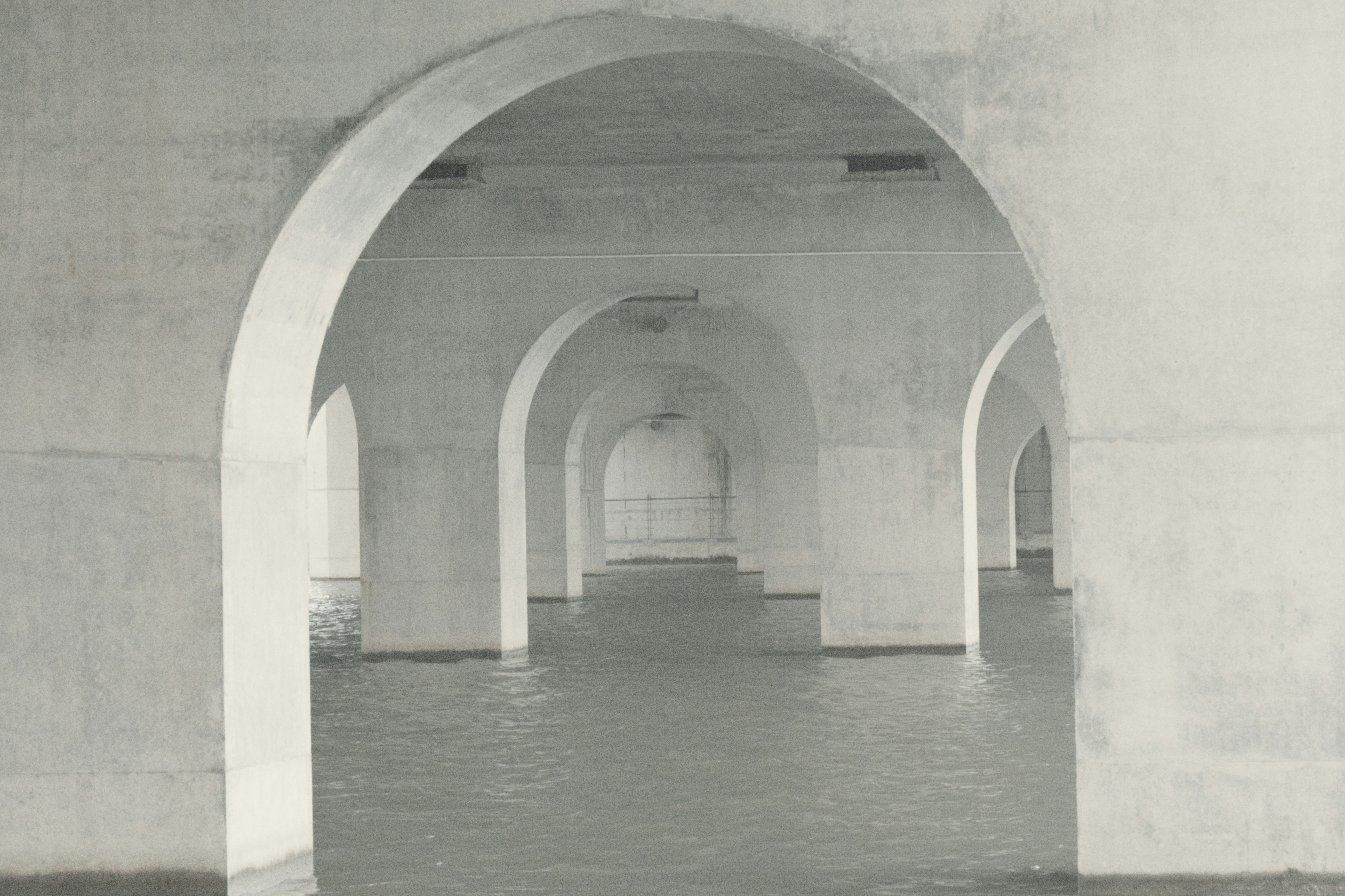 Repetitive concrete arches create a visual rhythm over a reflective water surface.