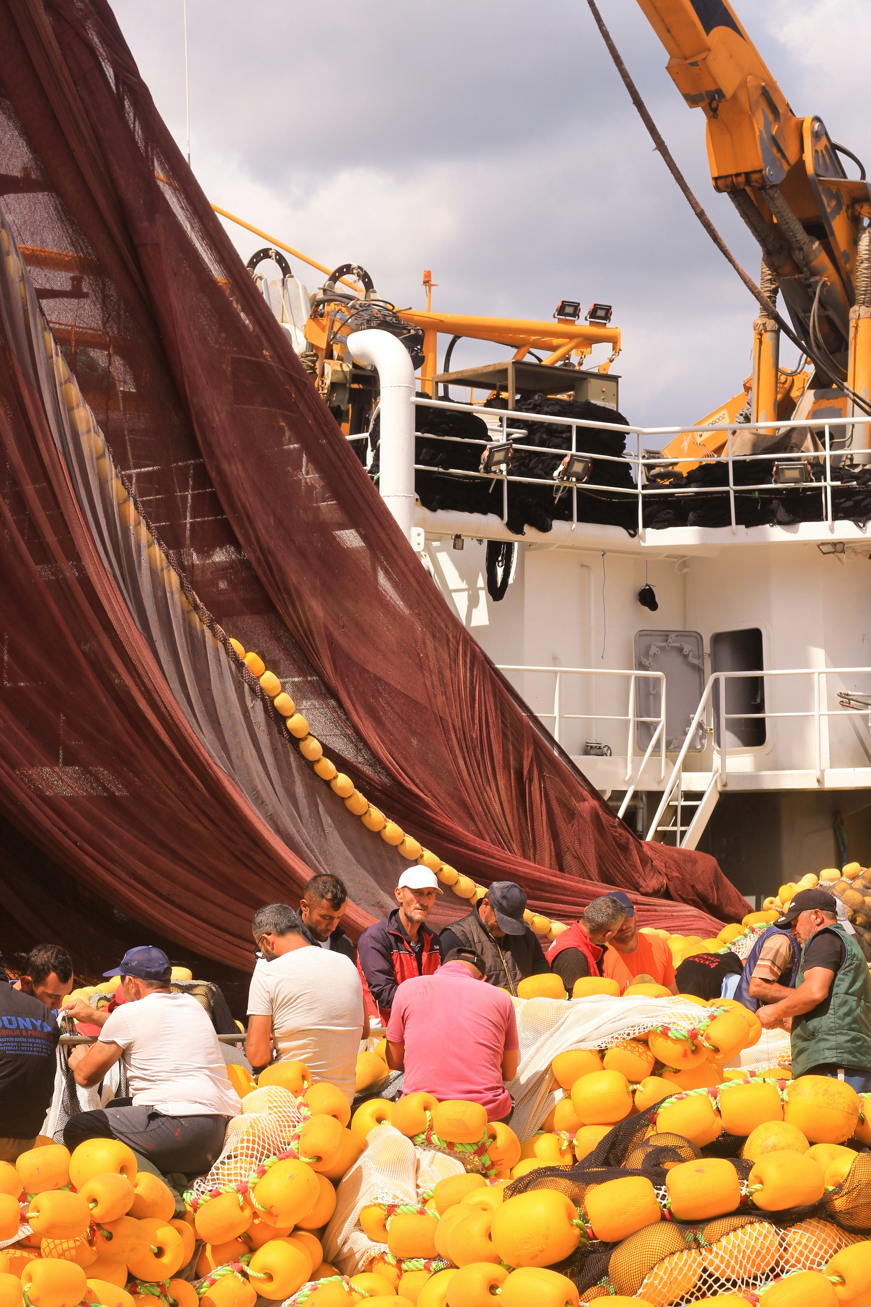 Crew at Work: Collecting Buoys Under Red Netting on a Vessel