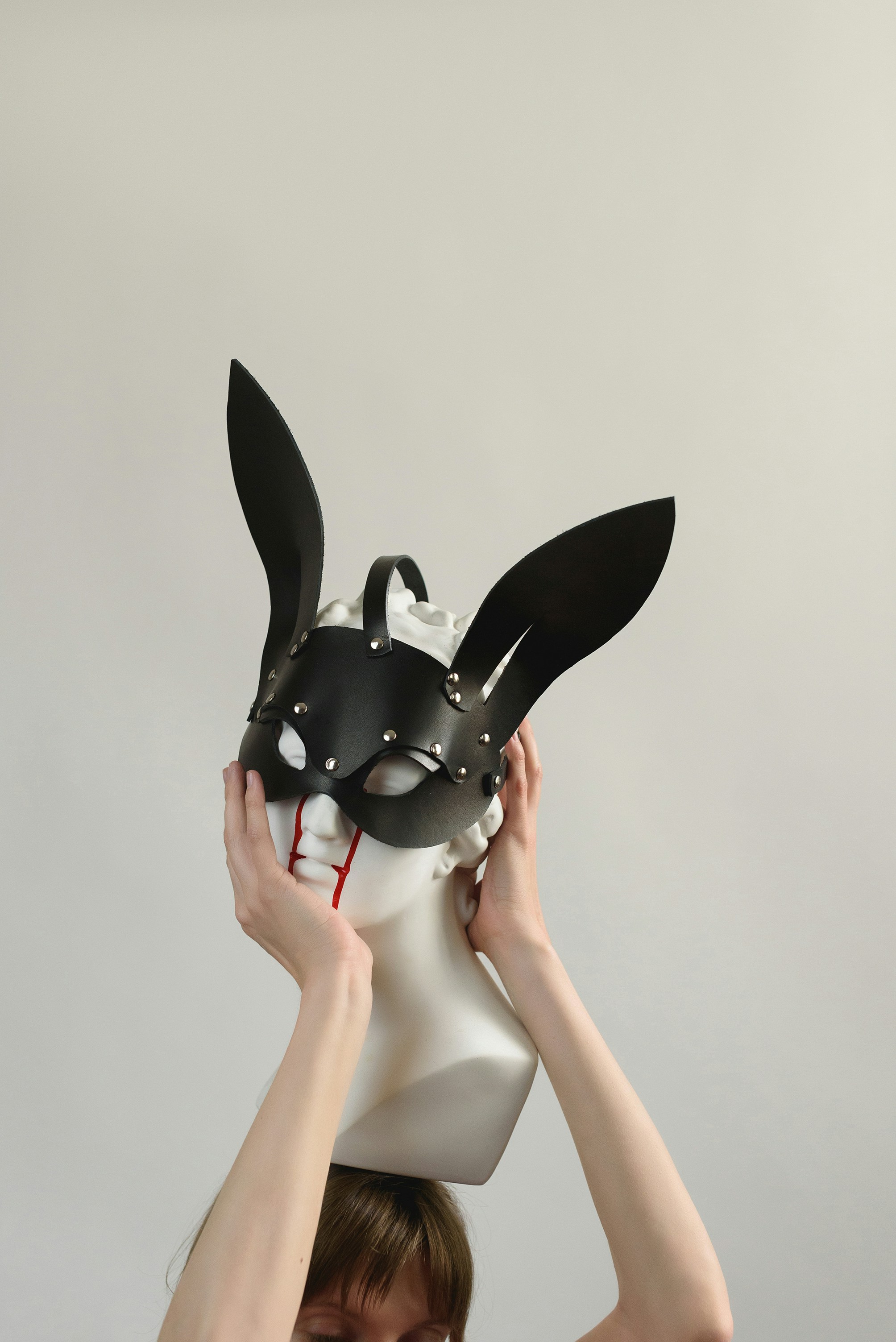A mannequin showcases a striking black bunny mask, held by a person, against a minimalist backdrop. The design features prominent ears and intricate detailing.