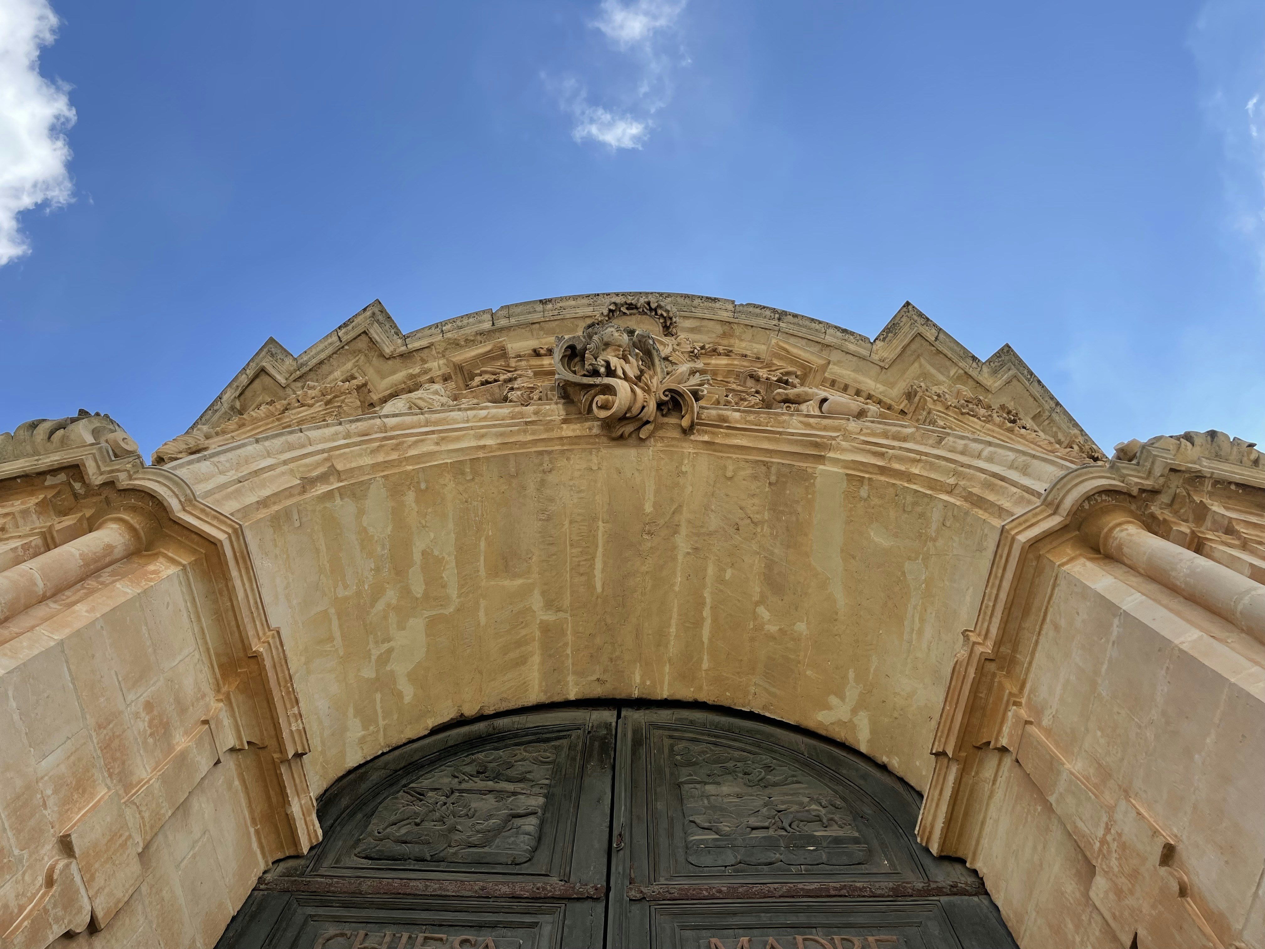 Intricate stonework and a grand entrance frame the sky above, showcasing historical architecture. The ornate crest adds a touch of artistry.