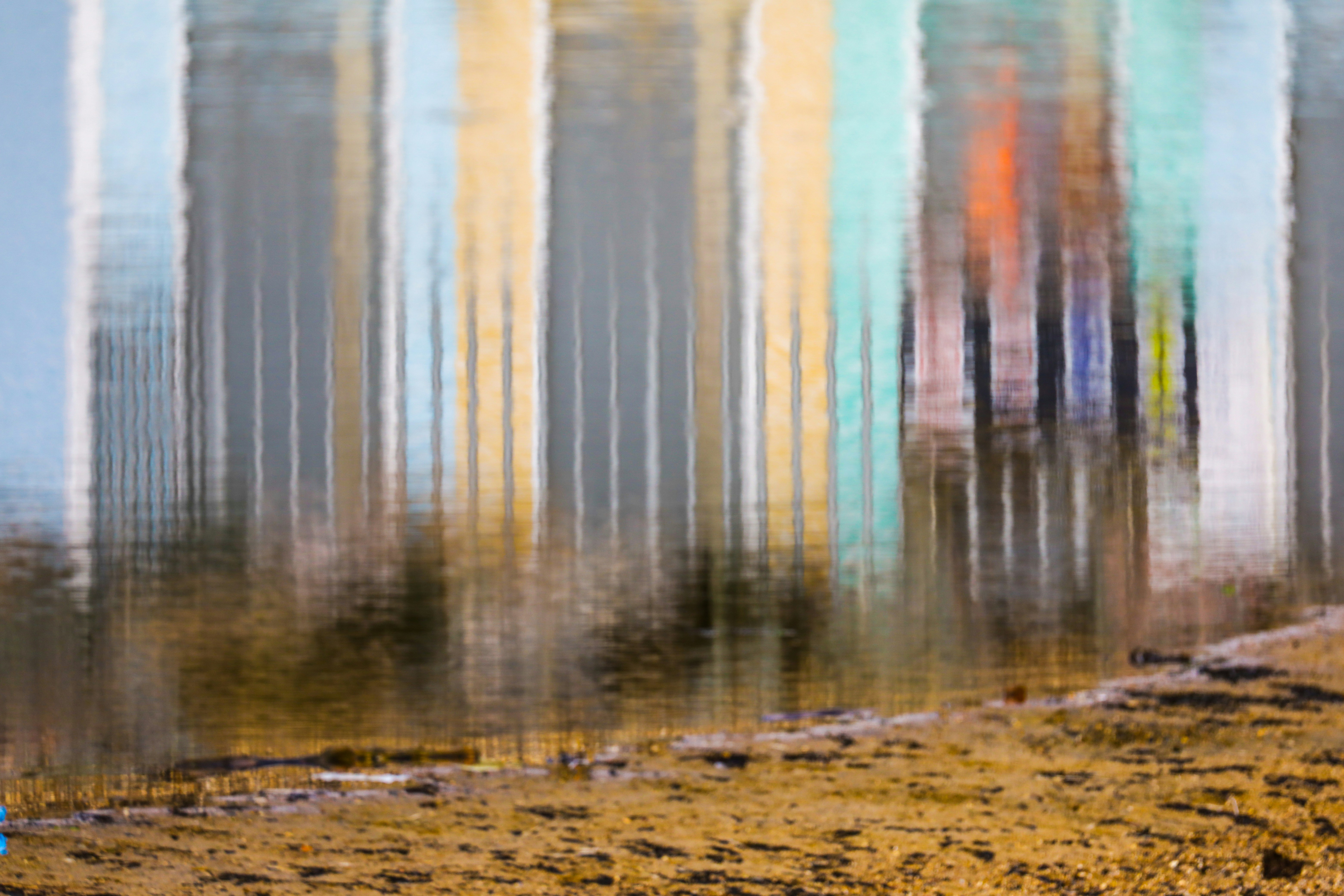 Vibrant reflections of buildings shimmer on the water's surface, creating a dreamlike effect near the sandy shore.