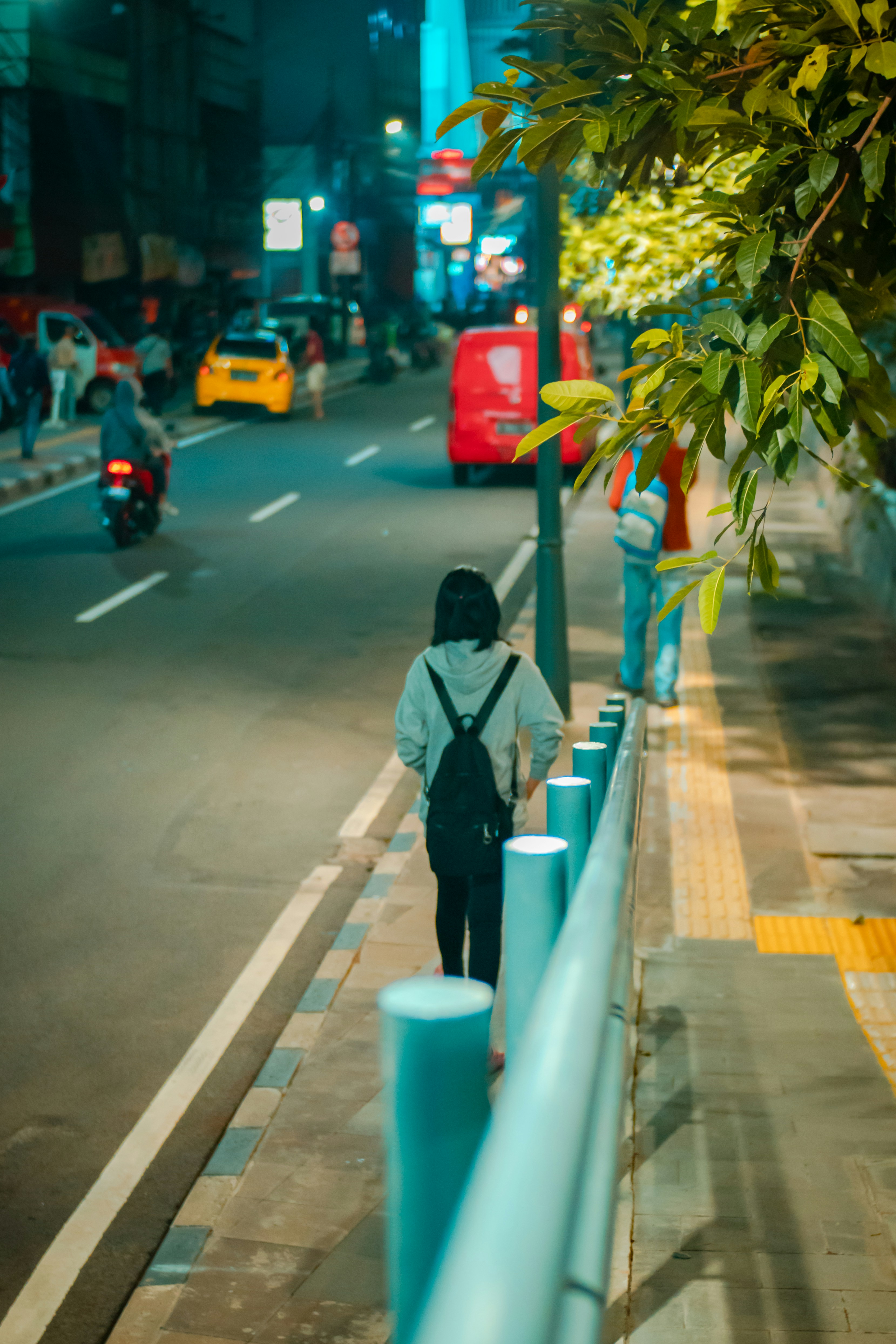 Night Walk Along Neon-Blue Railing: A Figure with Backpack Traverses a City Street