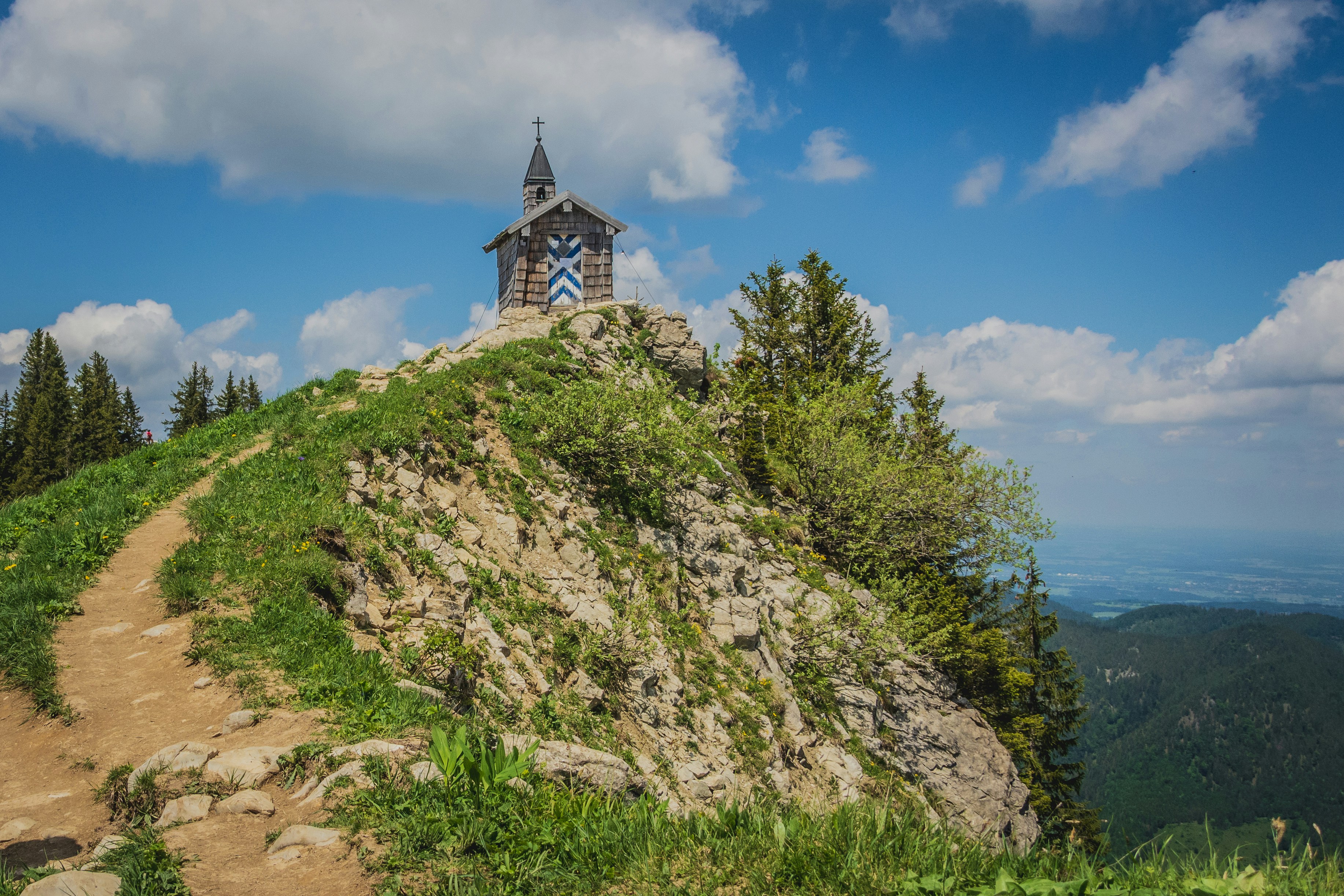 Chapel perched on a grassy hilltop under a vibrant blue sky with scattered clouds.