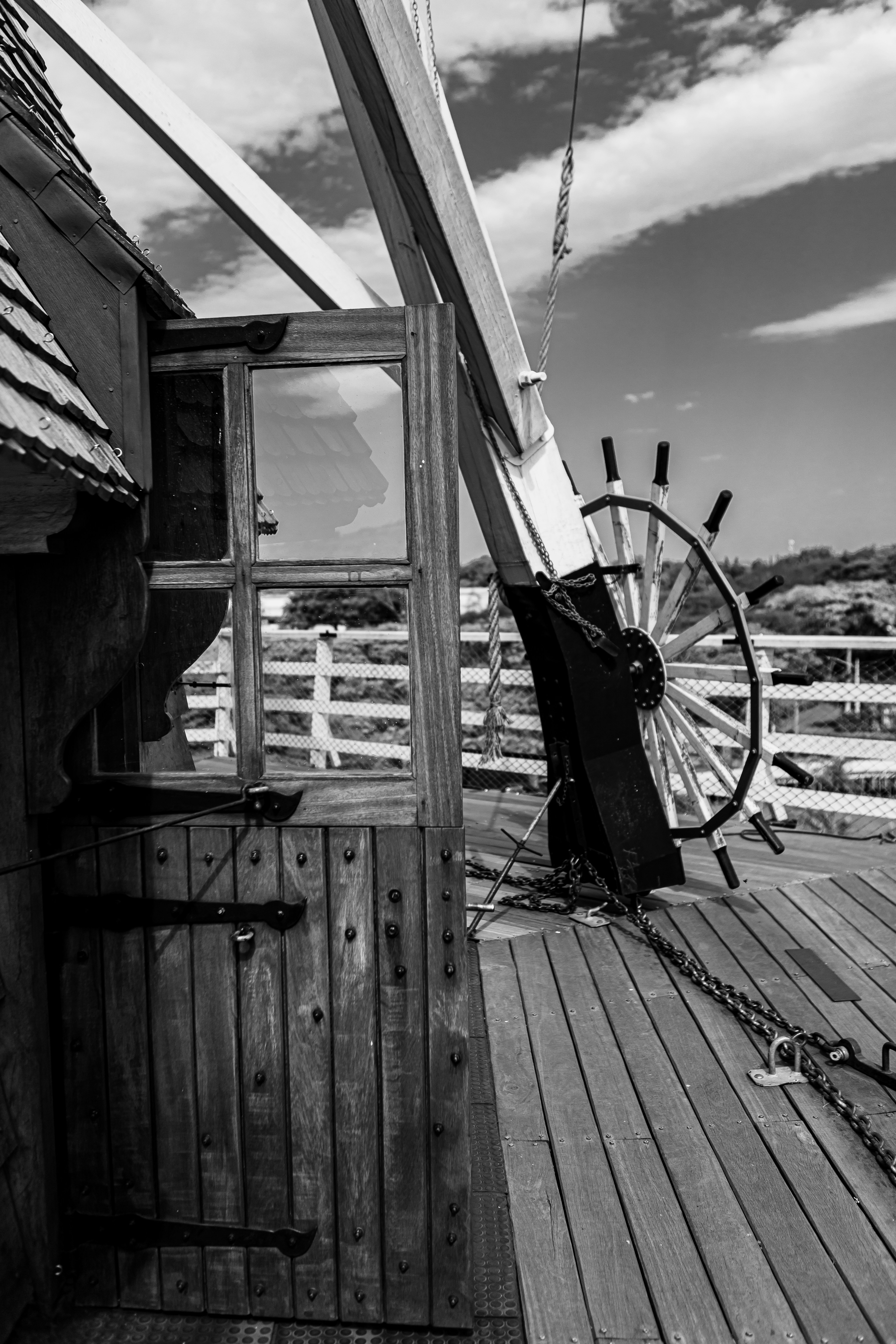 Weathered wooden cabin window revealing a ship's wheel and deck, evoking the spirit of seafaring adventures.