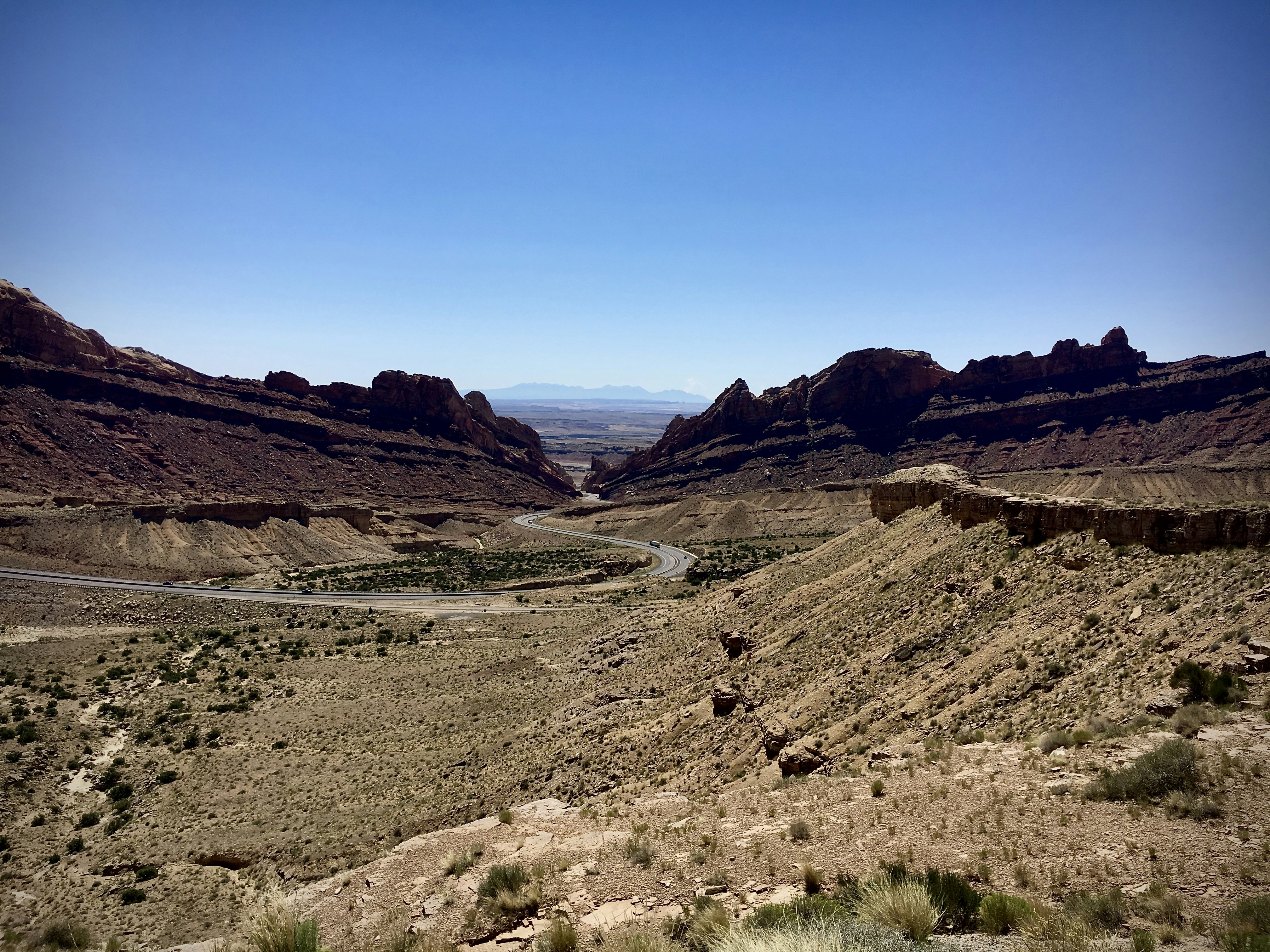Curving road meanders through rugged canyon landscape under a clear blue sky.