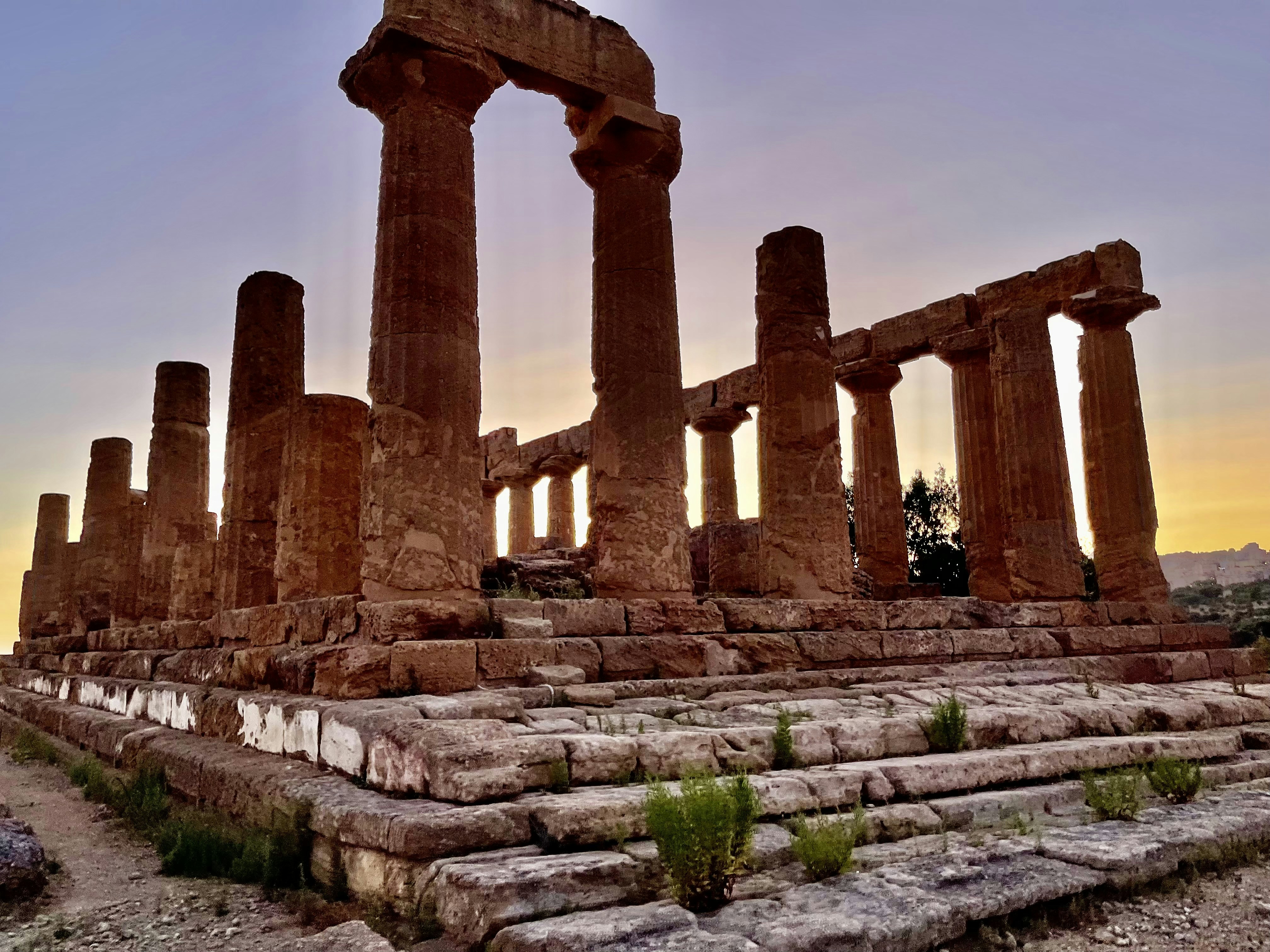 Stone columns of a historic temple silhouetted against a vibrant sunset sky.