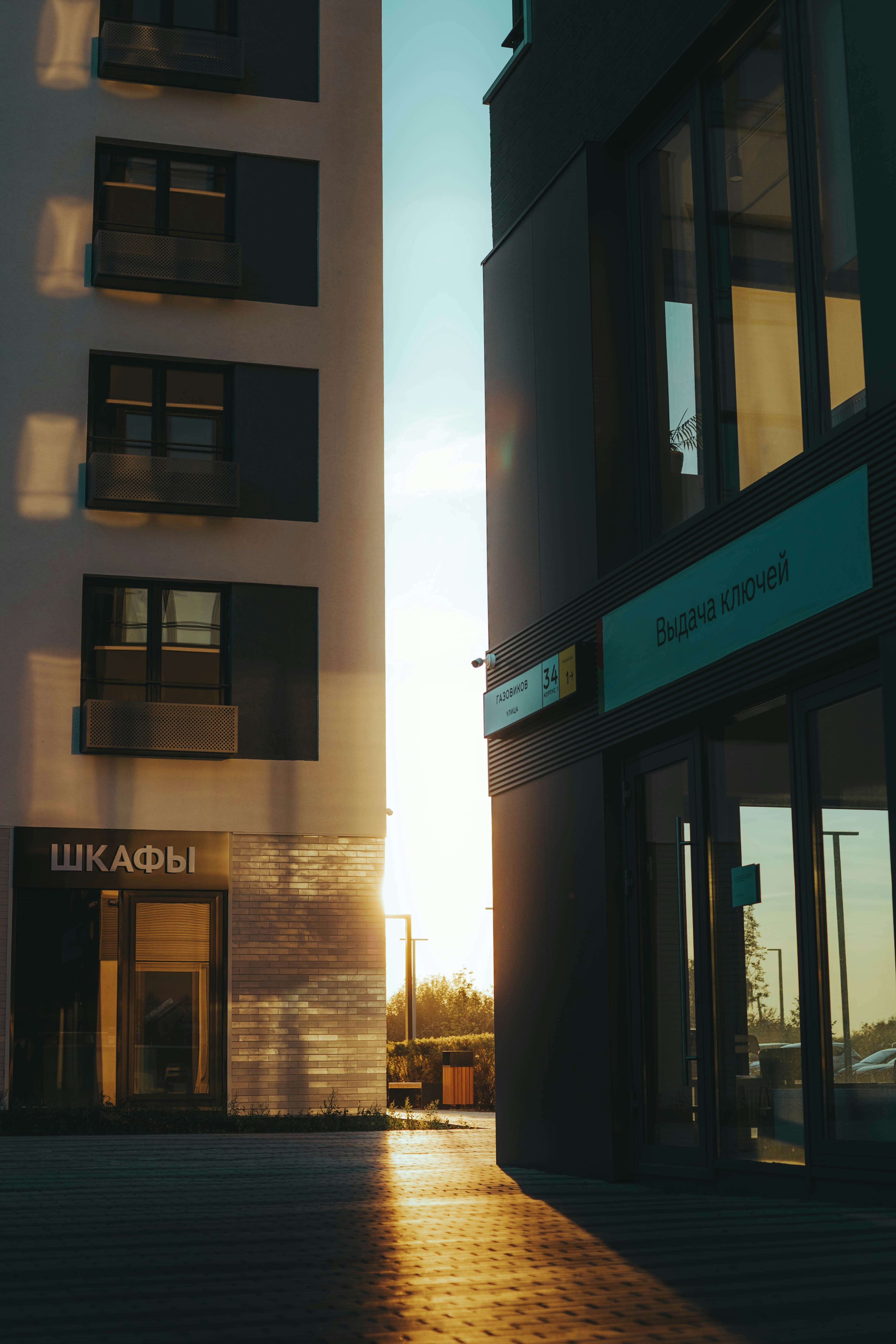 Modern buildings casting soft shadows under the warm glow of a setting sun, highlighting architectural details and urban life.