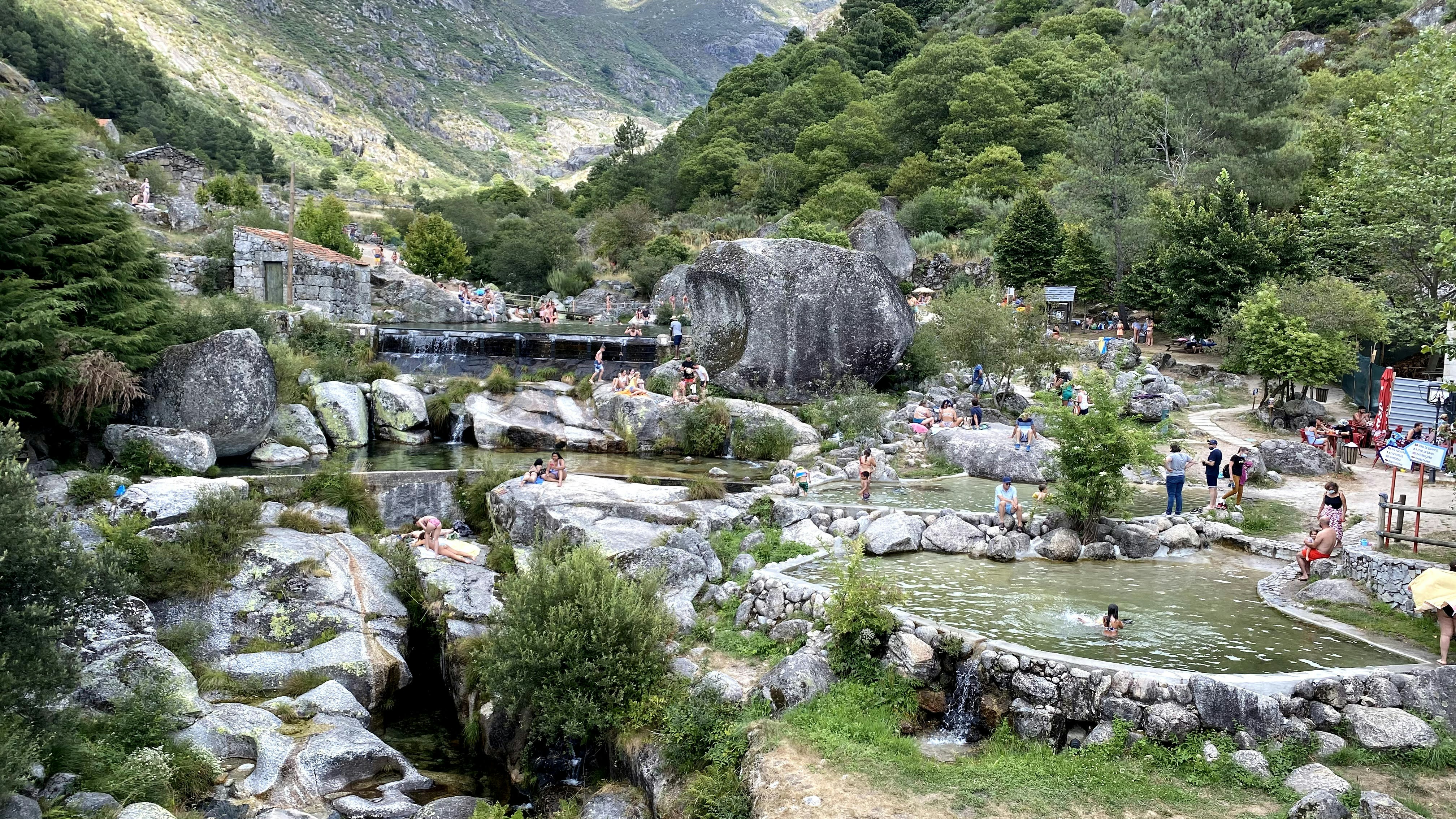 Visitors enjoying thermal pools surrounded by lush greenery and rocky landscapes. The scene captures a harmonious blend of nature and relaxation.