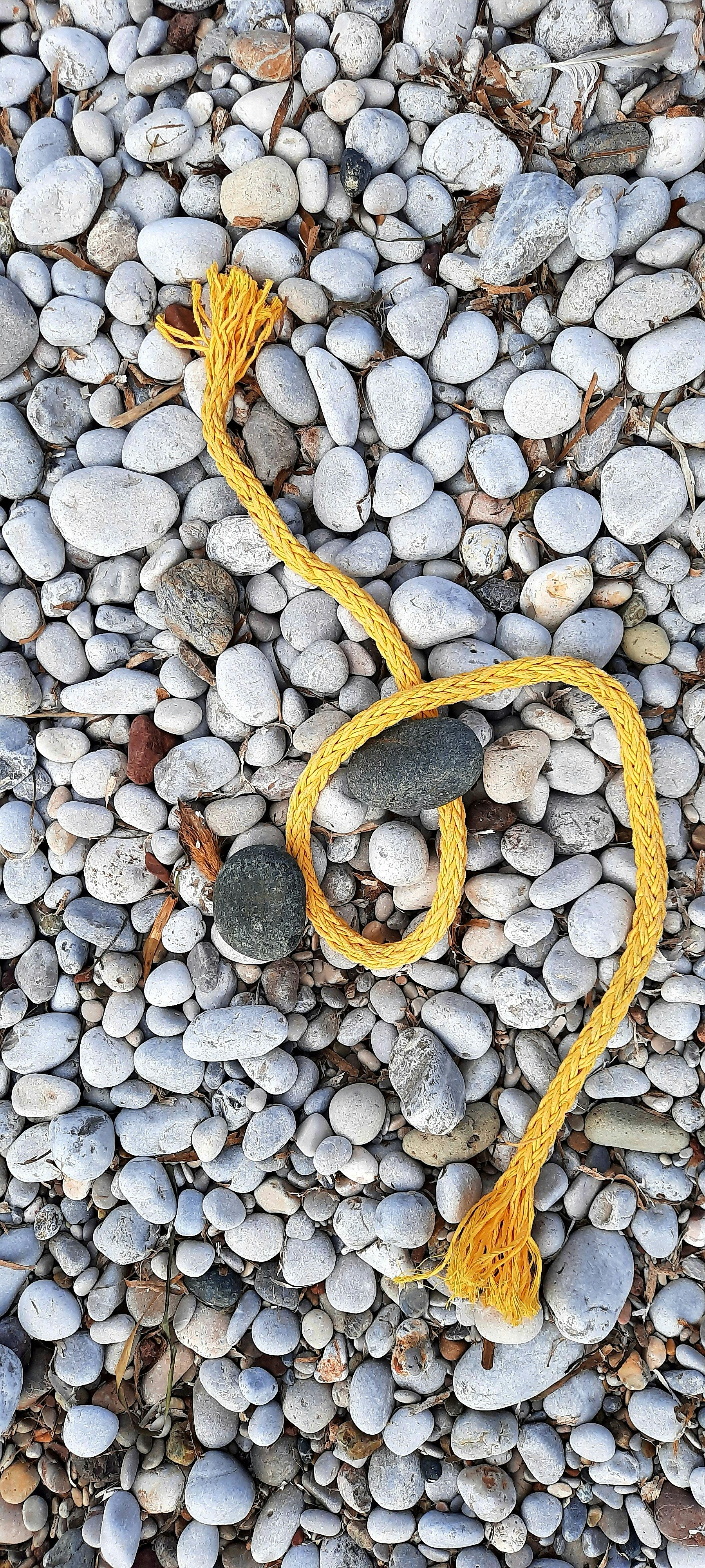 A yellow rope intertwined with smooth stones on a pebbled surface, showcasing a blend of natural textures and colors.