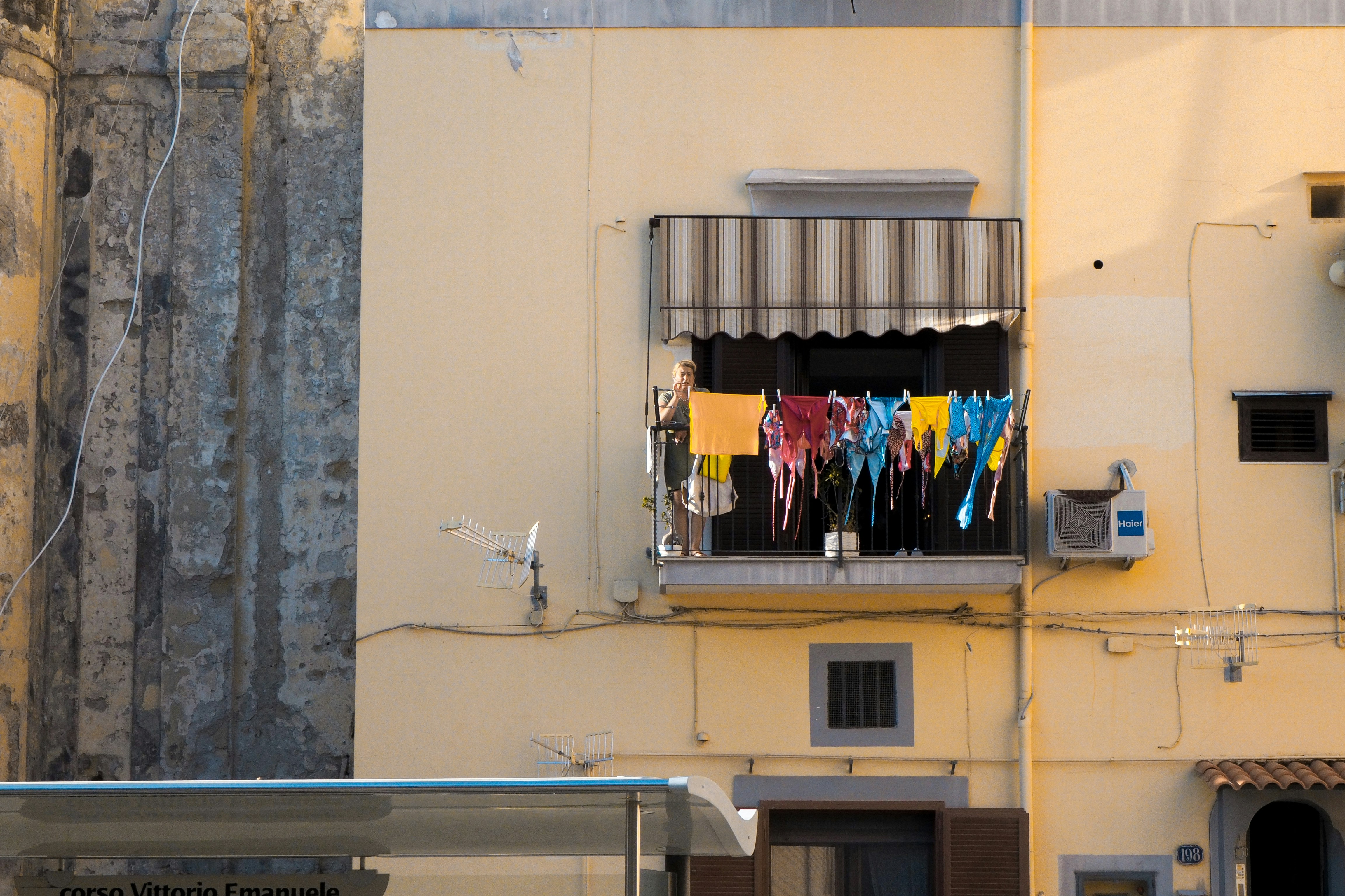 Colorful clothes hanging from a balcony in a charming urban setting, showcasing a blend of daily life and vibrant hues. The warm sunlight enhances the scene.