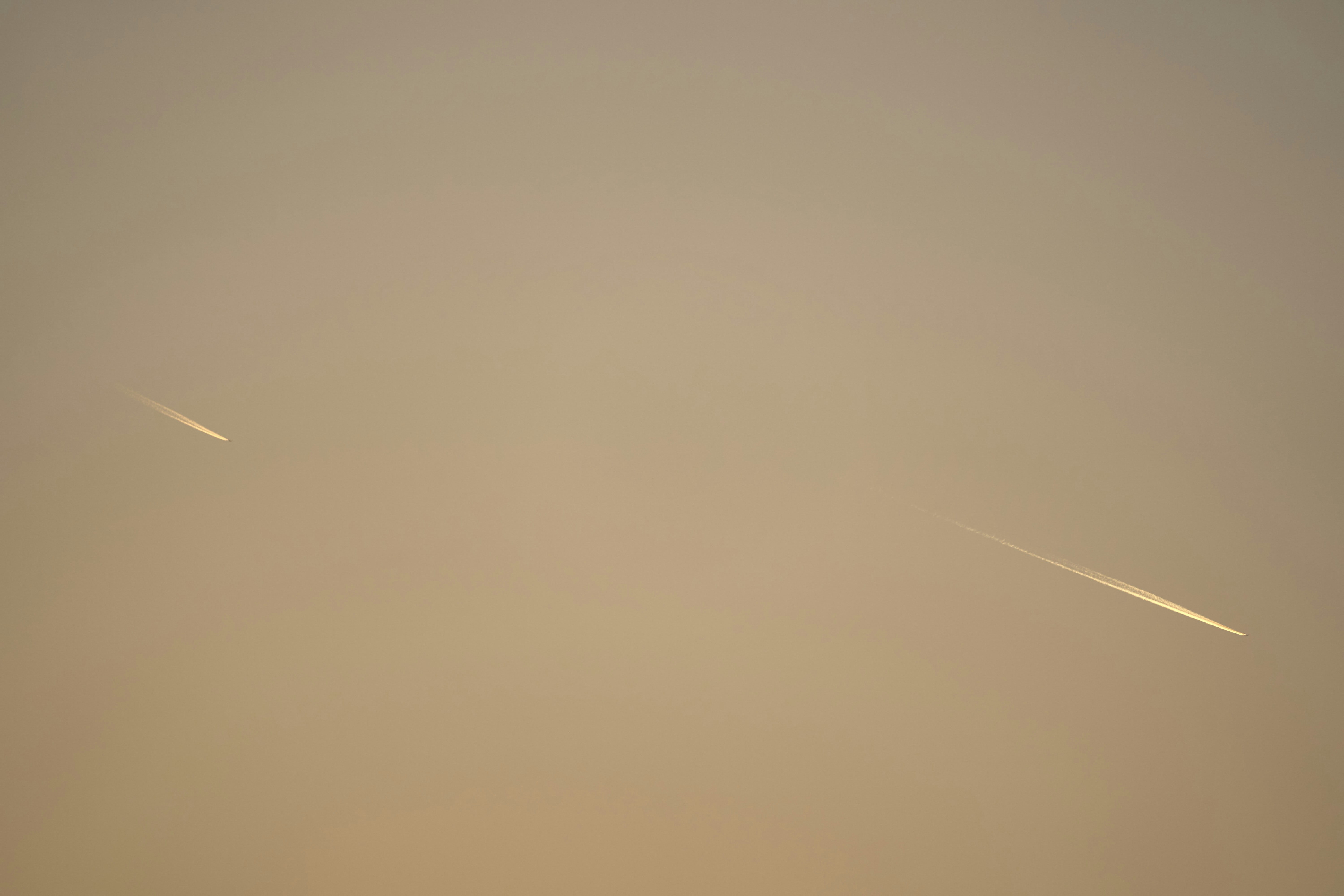 Two faint contrails streaking across a soft, pastel sky at dusk.