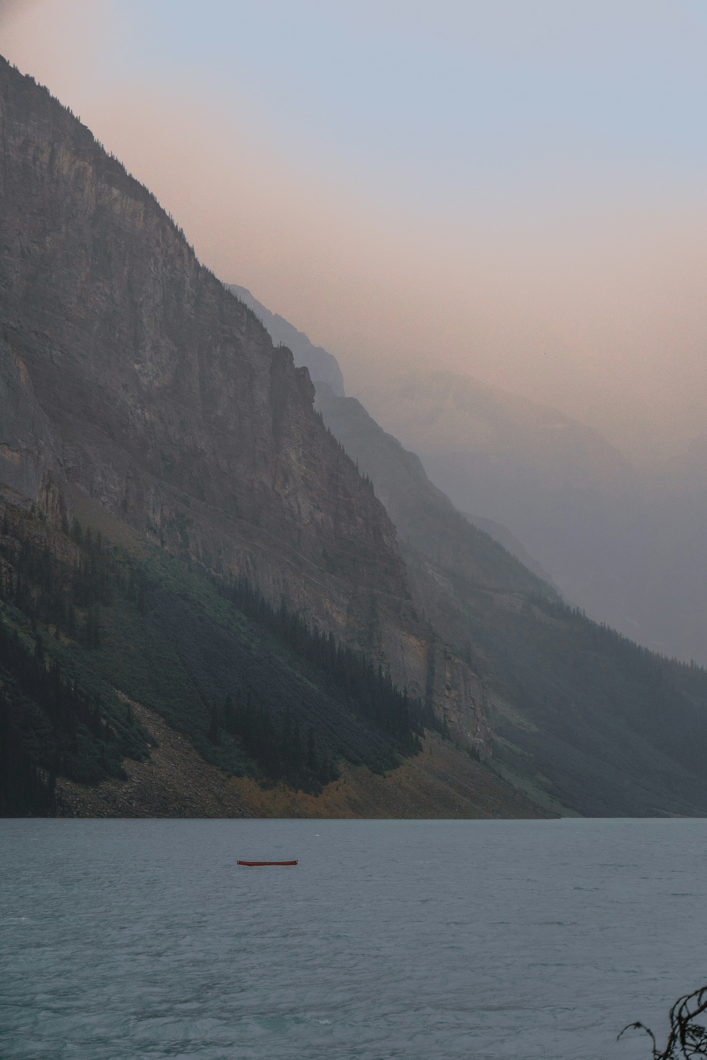Mist over a tranquil alpine lake with a lone red canoe