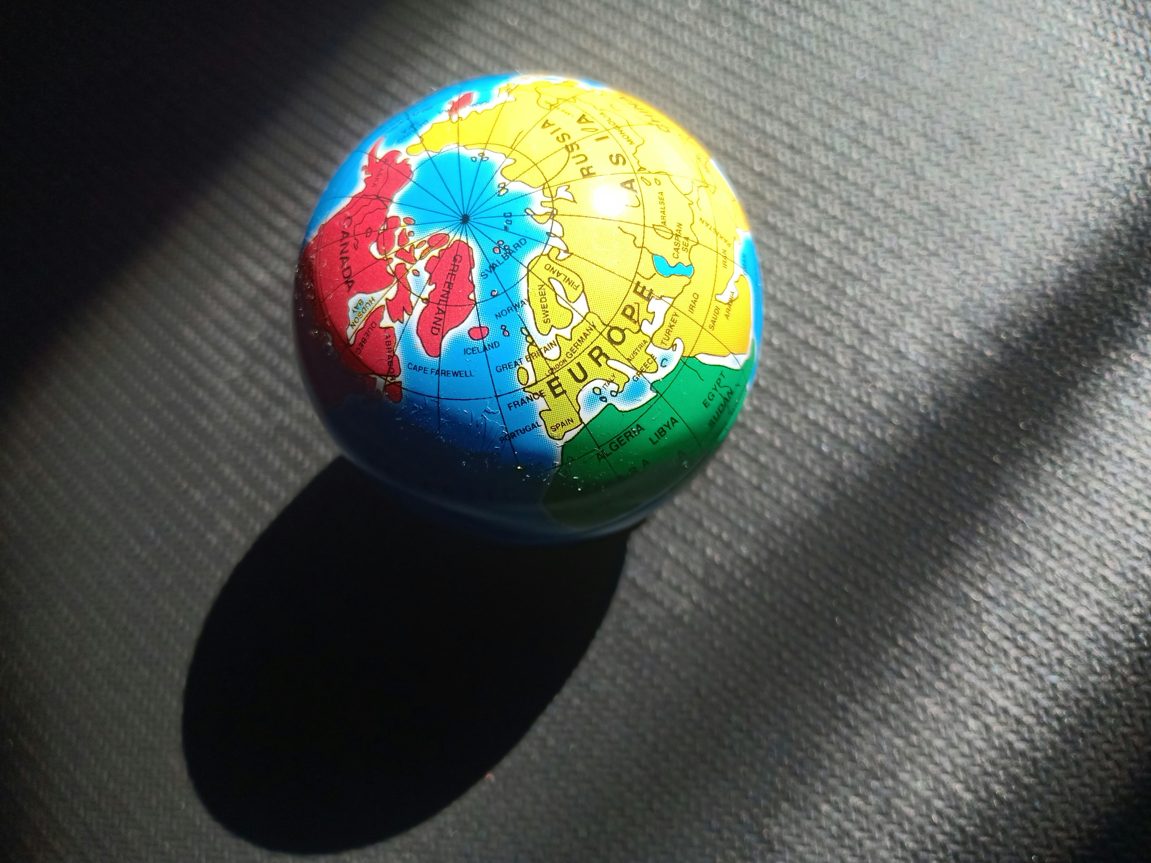 Colorful globe highlighting Europe with distinct country borders and geographical features. The globe casts a soft shadow on a textured surface.
