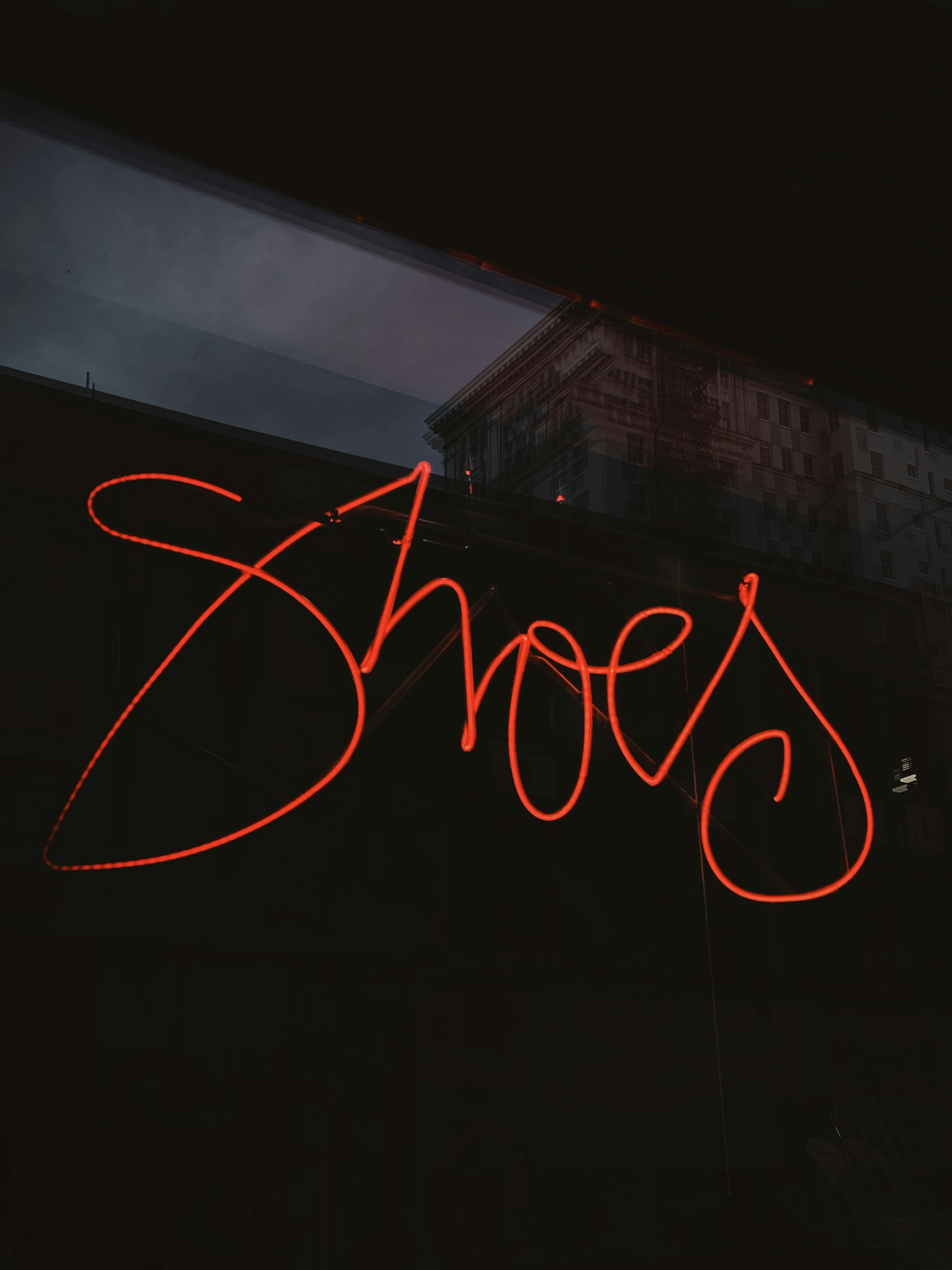 Neon sign spelling 'Shoes' reflected in a shop window, capturing the essence of urban fashion culture.