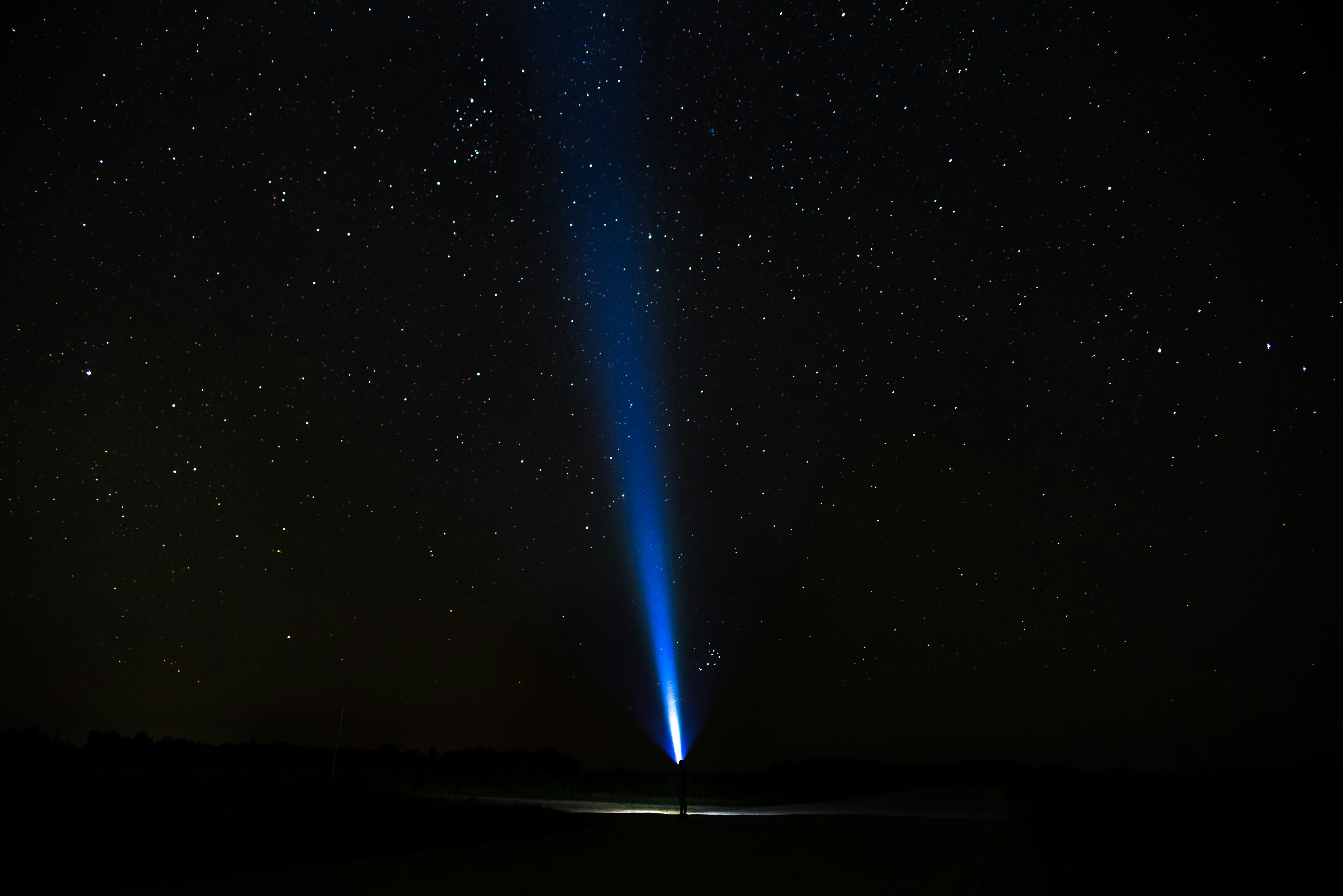 A powerful beam of light pierces the starry night, illuminating the surrounding darkness with a striking blue hue.