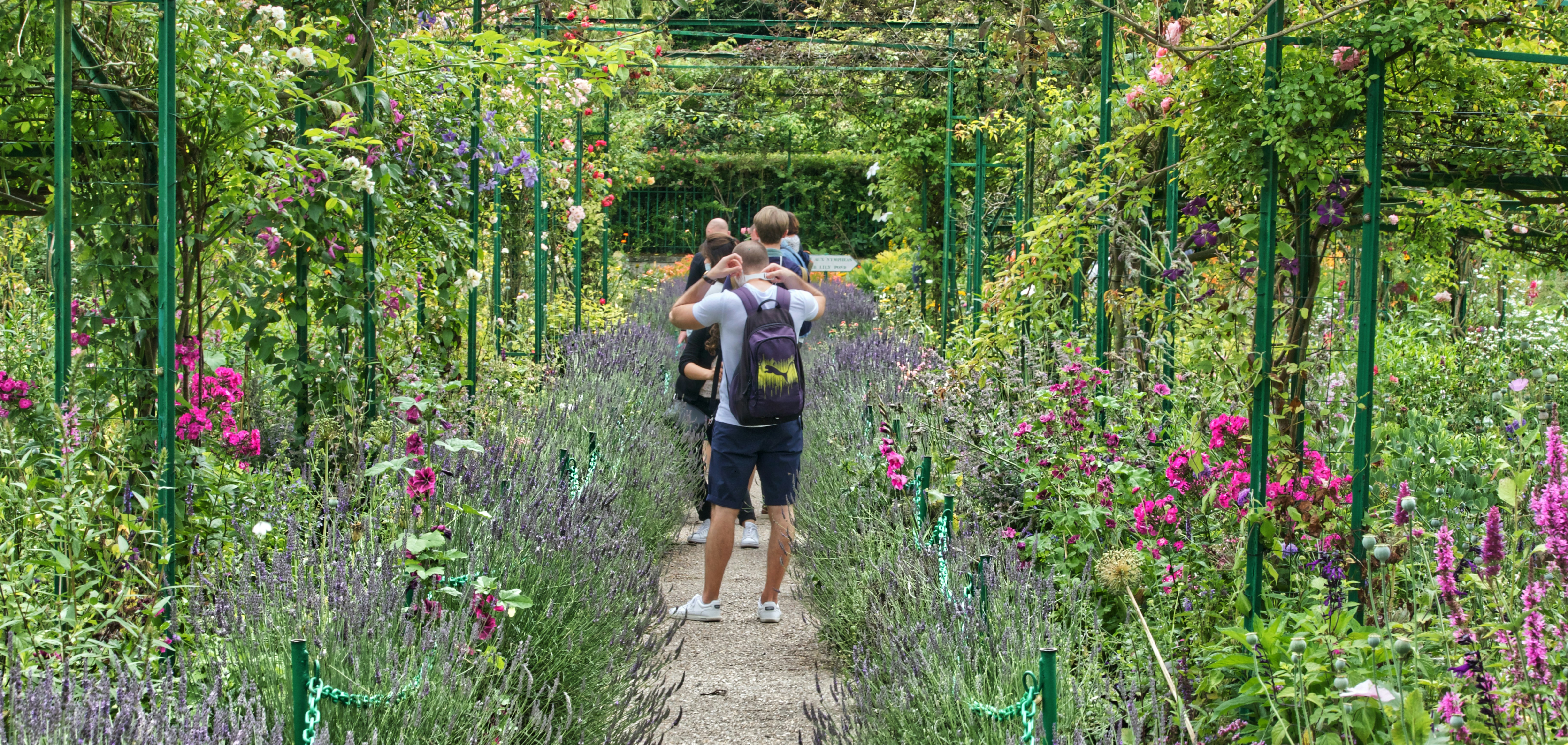 Visitors stroll through a vibrant garden pathway lined with blooming flowers and lush greenery.