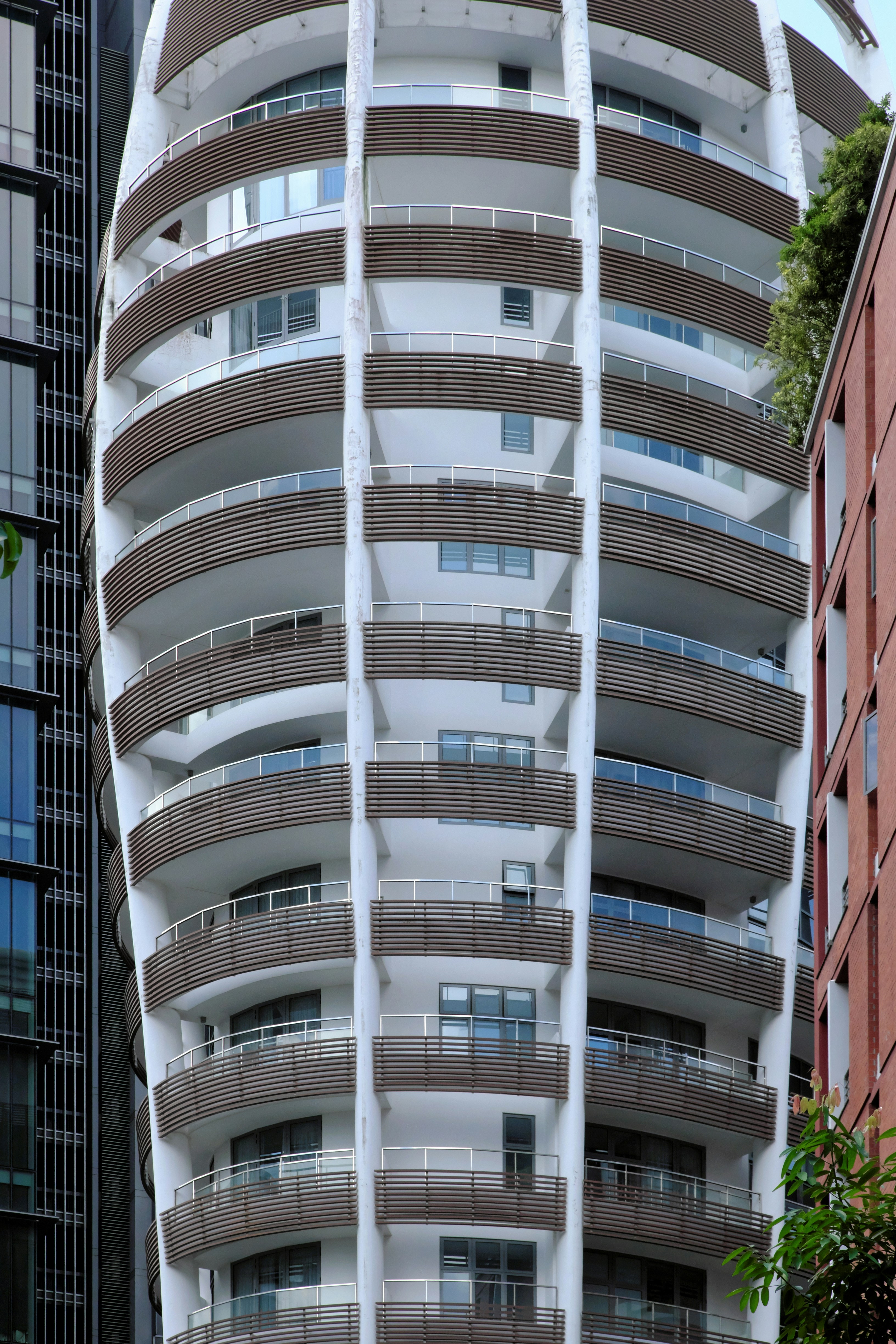 A modern residential building featuring a distinctive curvilinear design with multiple balconies and large windows, surrounded by contrasting structures.